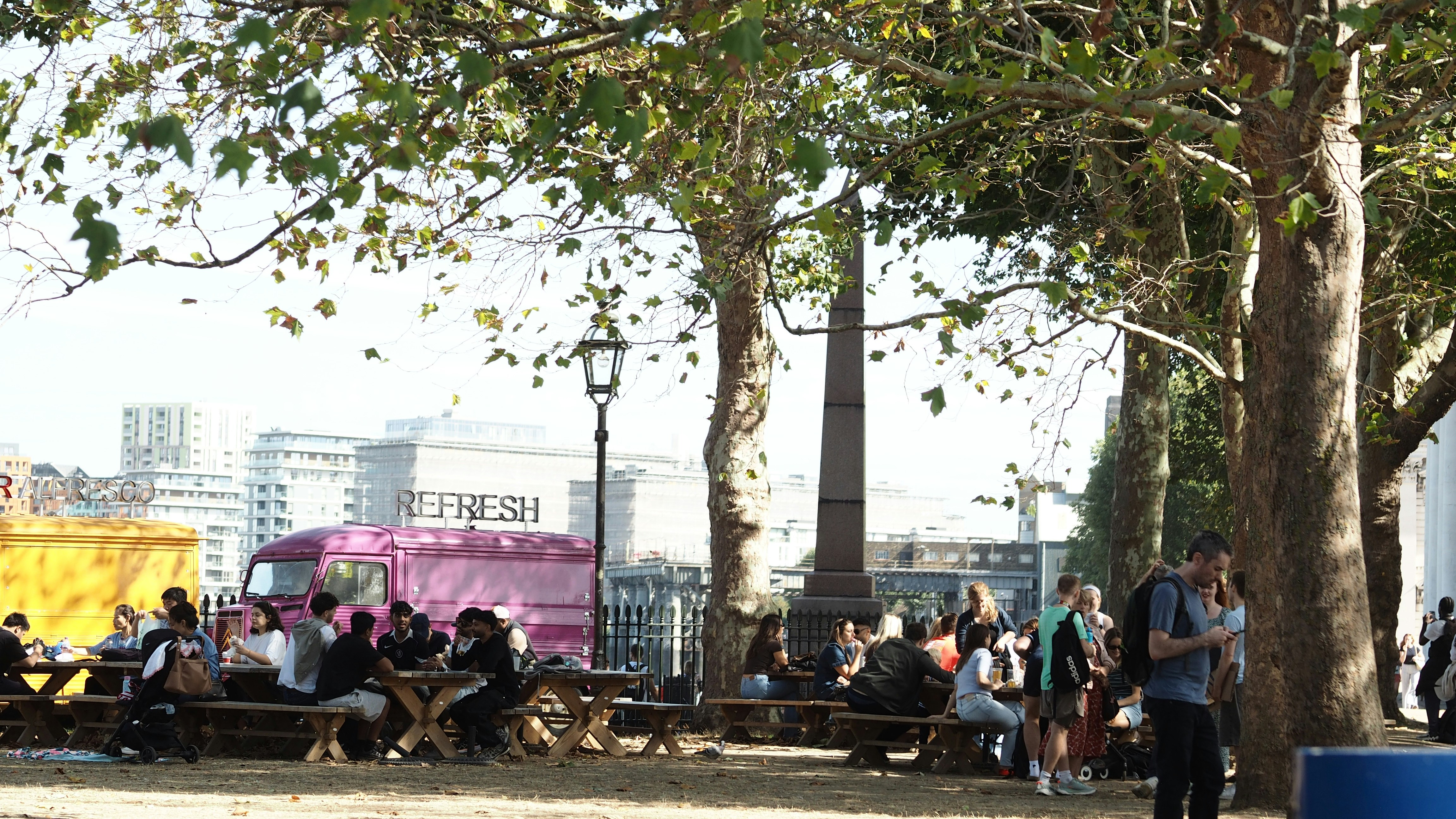 Lunch Break by the River: Social Scene Under Shaded Trees