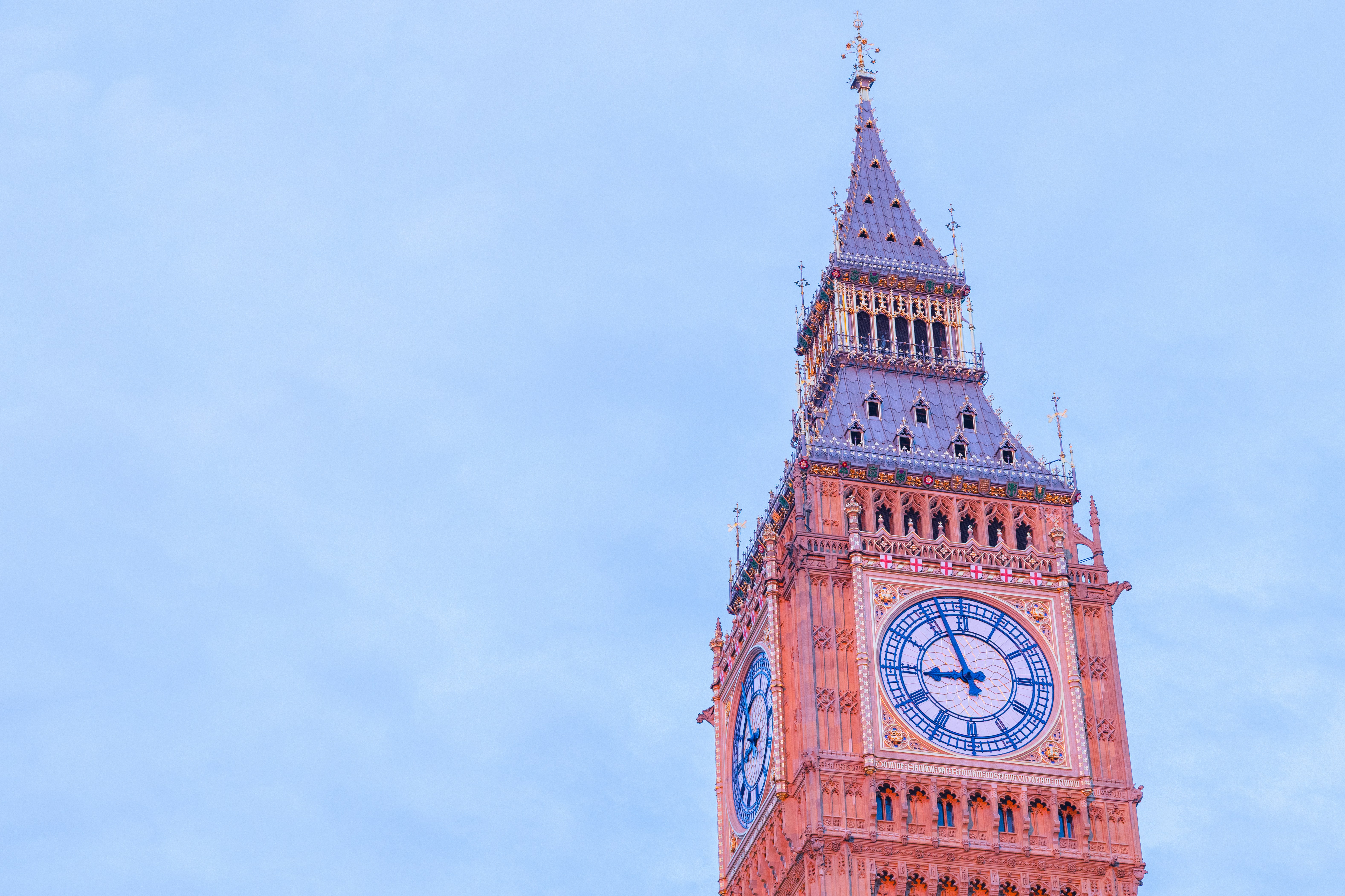 Tall clock tower rises against a pale blue sky, capturing the intricate facade and ornate spire.