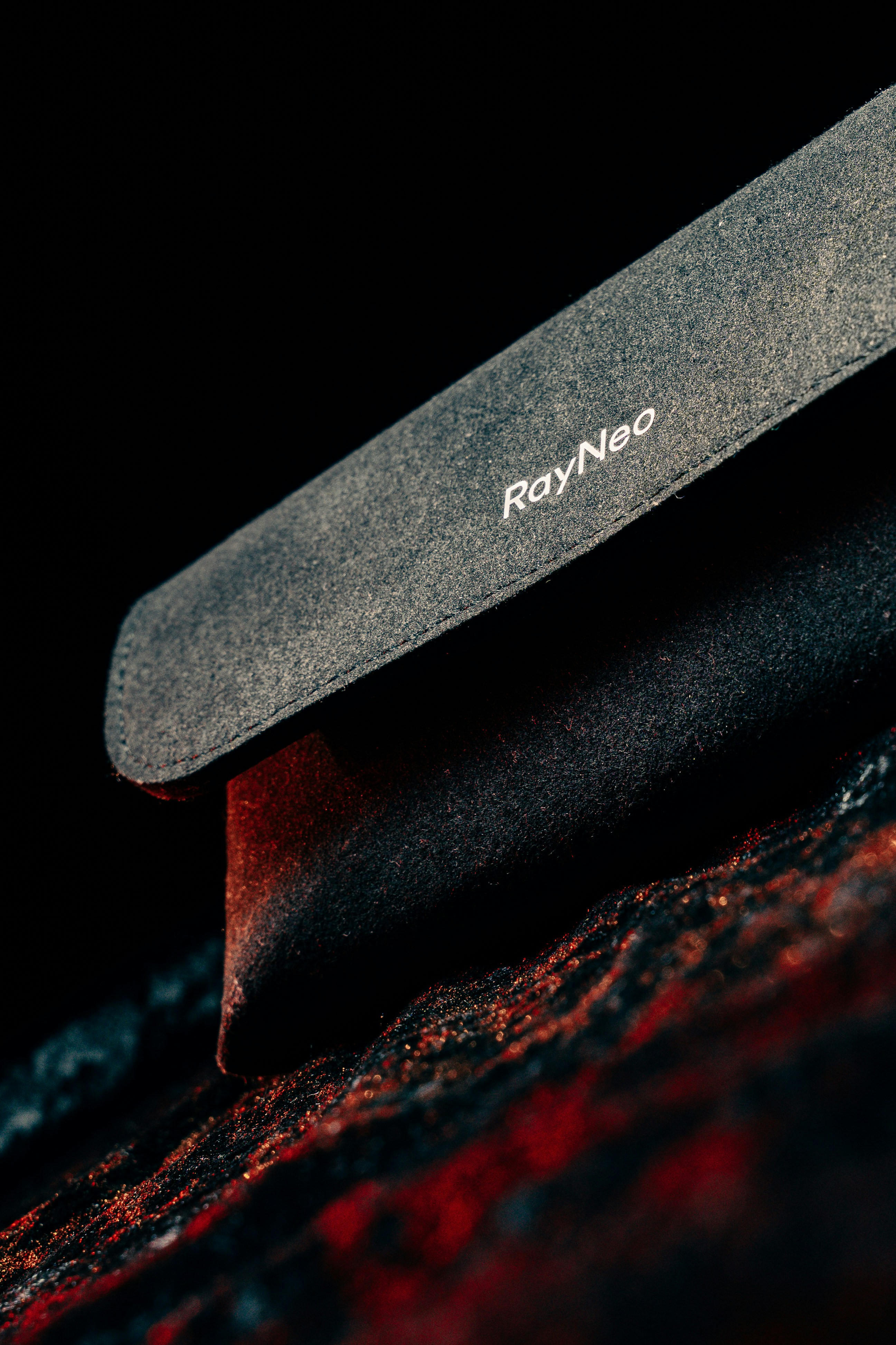 RayNeo etched in matte metal resting on a dark, gritty surface