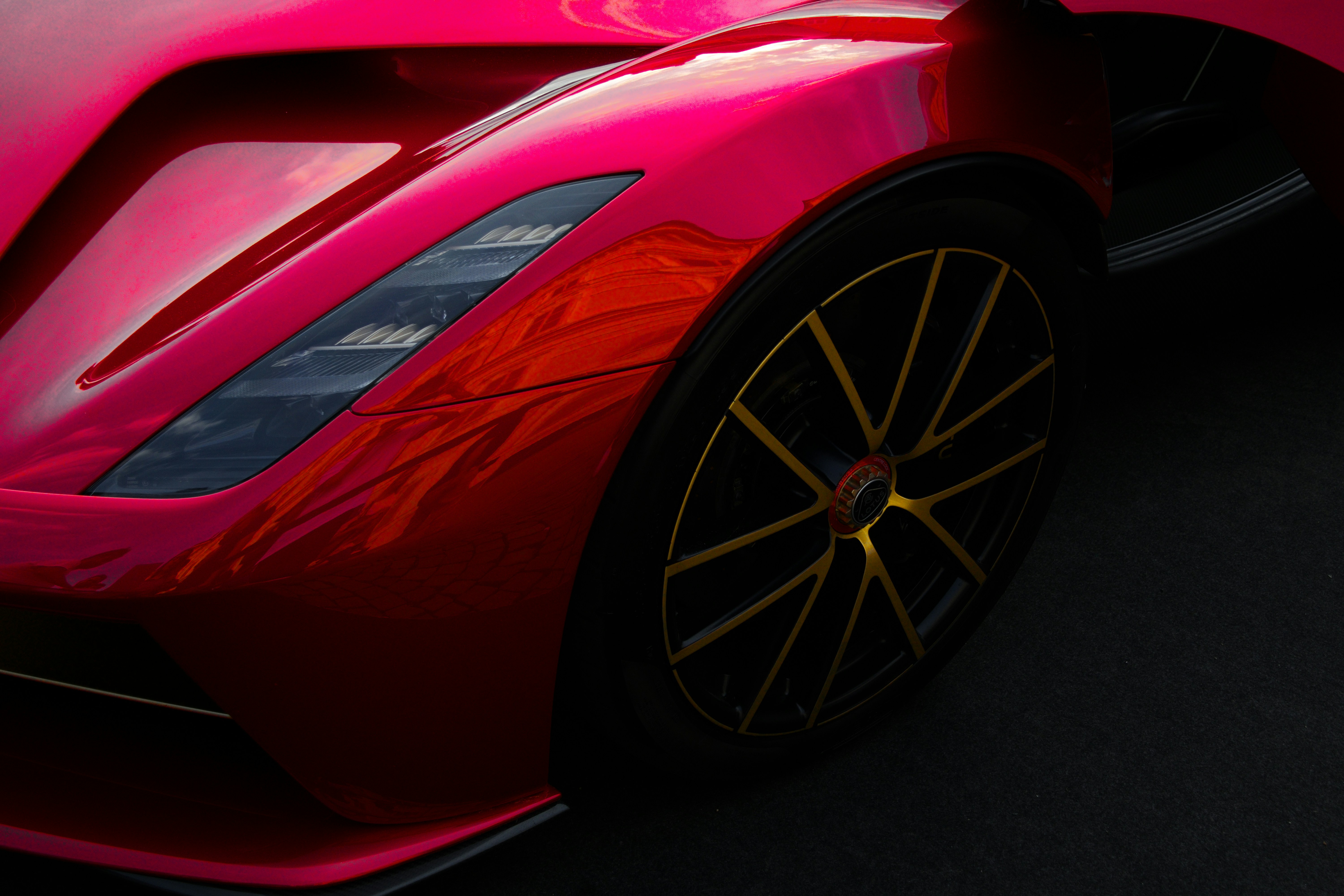 A glossy red sports car with gold and black wheels on asphalt
