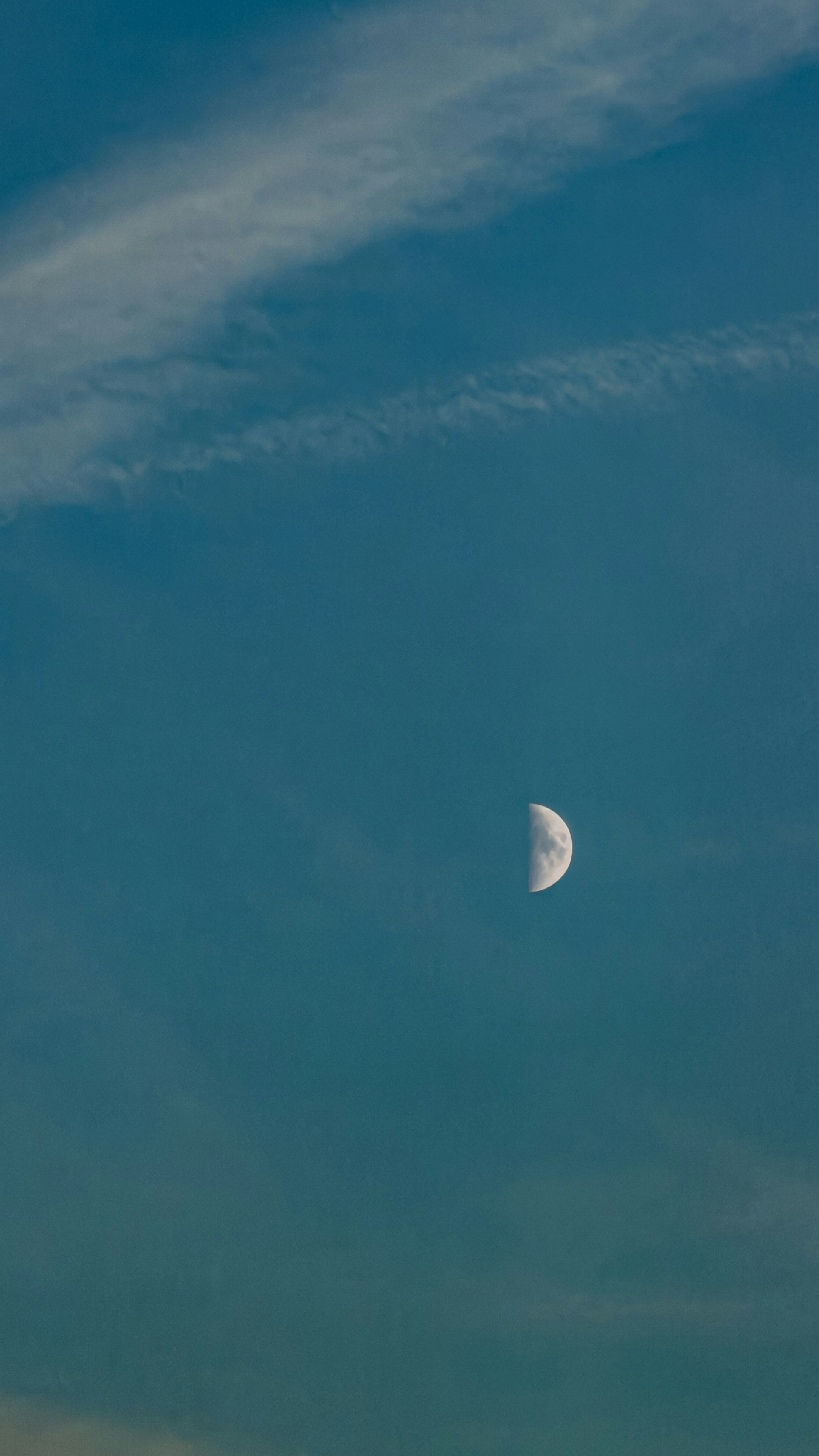A half moon in a clear blue sky with thin wispy clouds