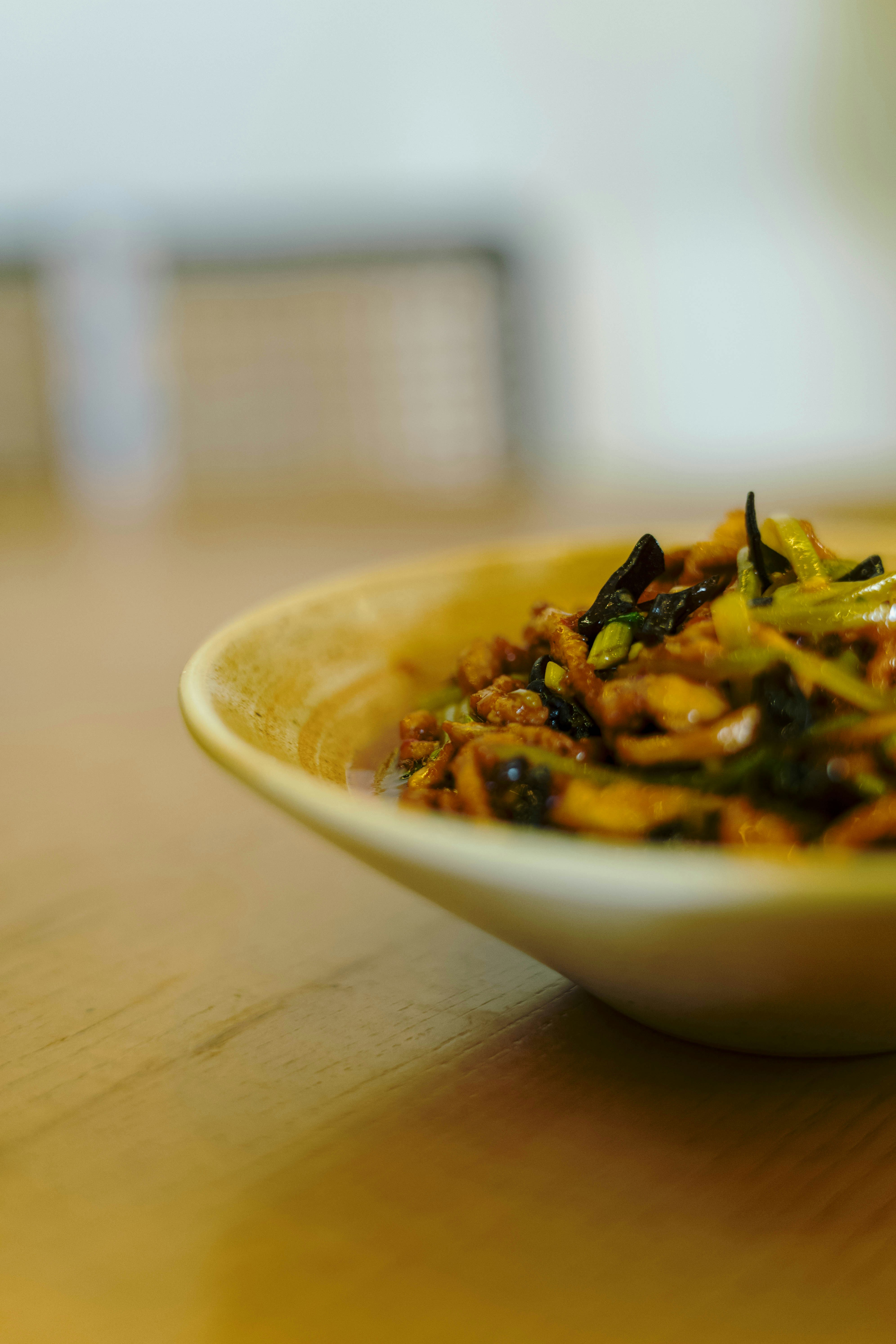 Close-up of a plated noodle dish on a wooden table, focusing on the savory toppings and glossy sauce. This is a food photograph capturing texture and color, suitable for menu or blog use.