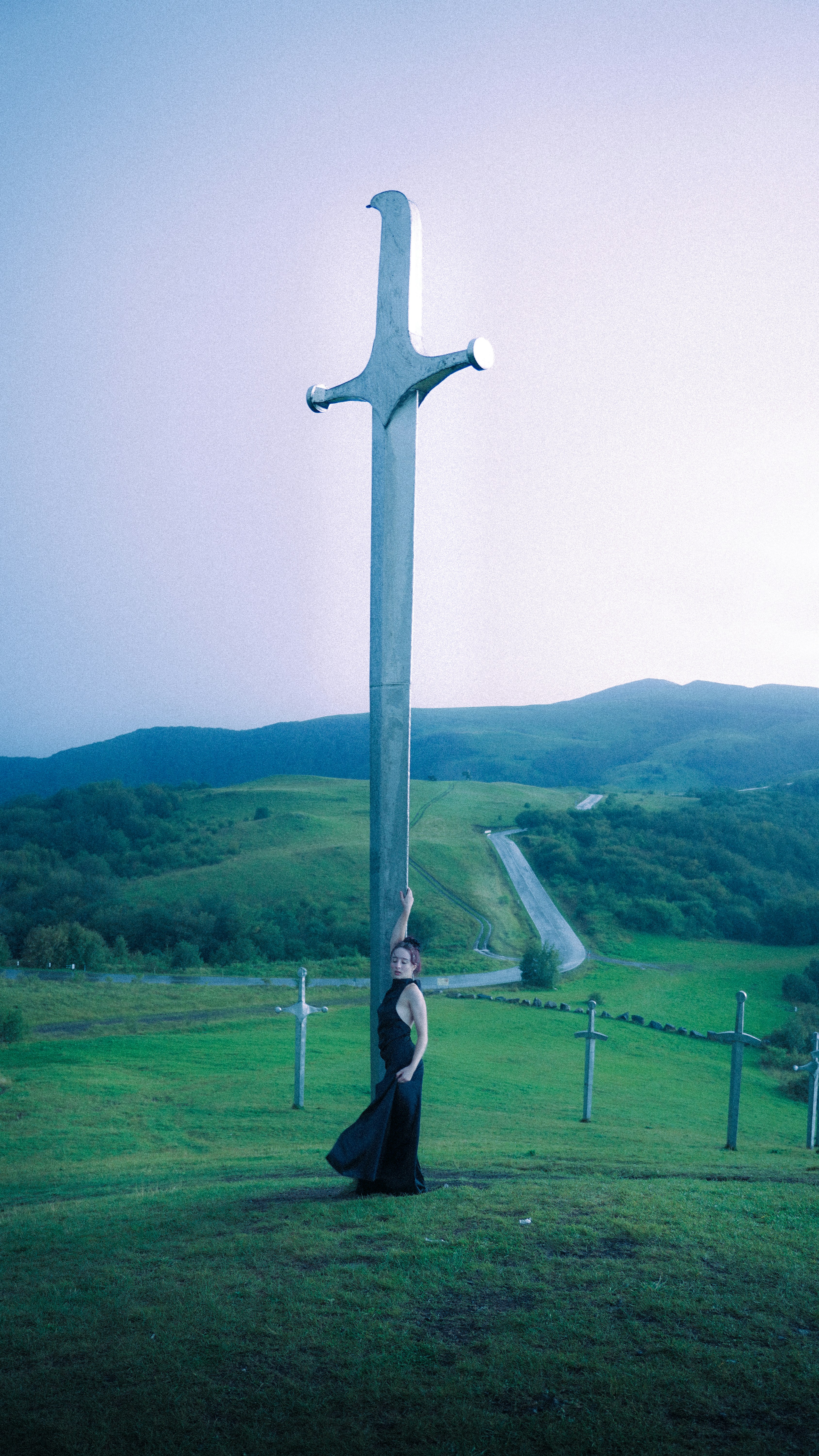 Crossroad of Hills: A Woman Clings to a Monument Under Wide Sky