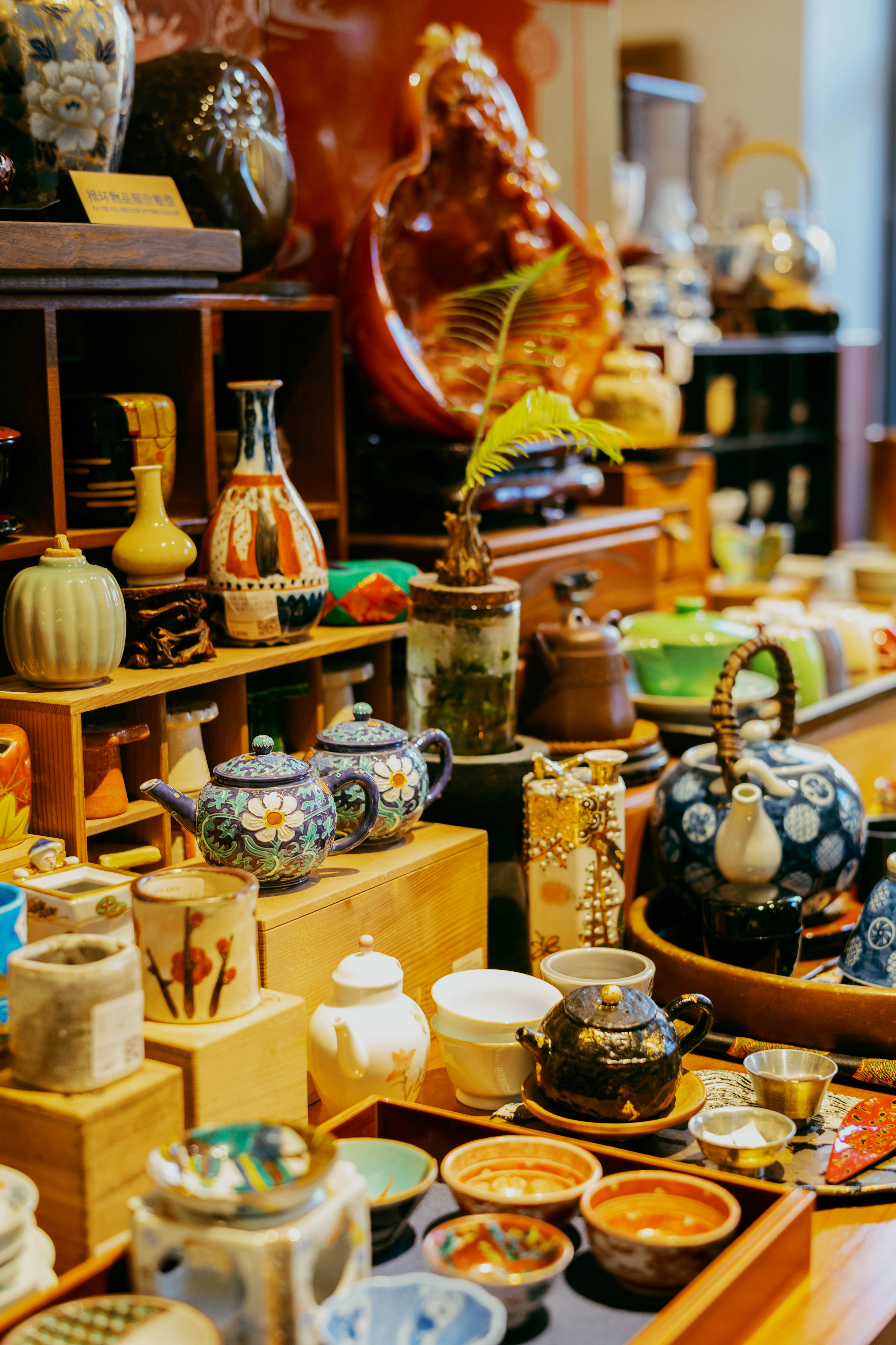 Colorful ceramic teapots and bowls fill a wooden display, creating a warm, busy still-life of craft items in an indoor shop. This is a detailed photograph of a decorative collection.