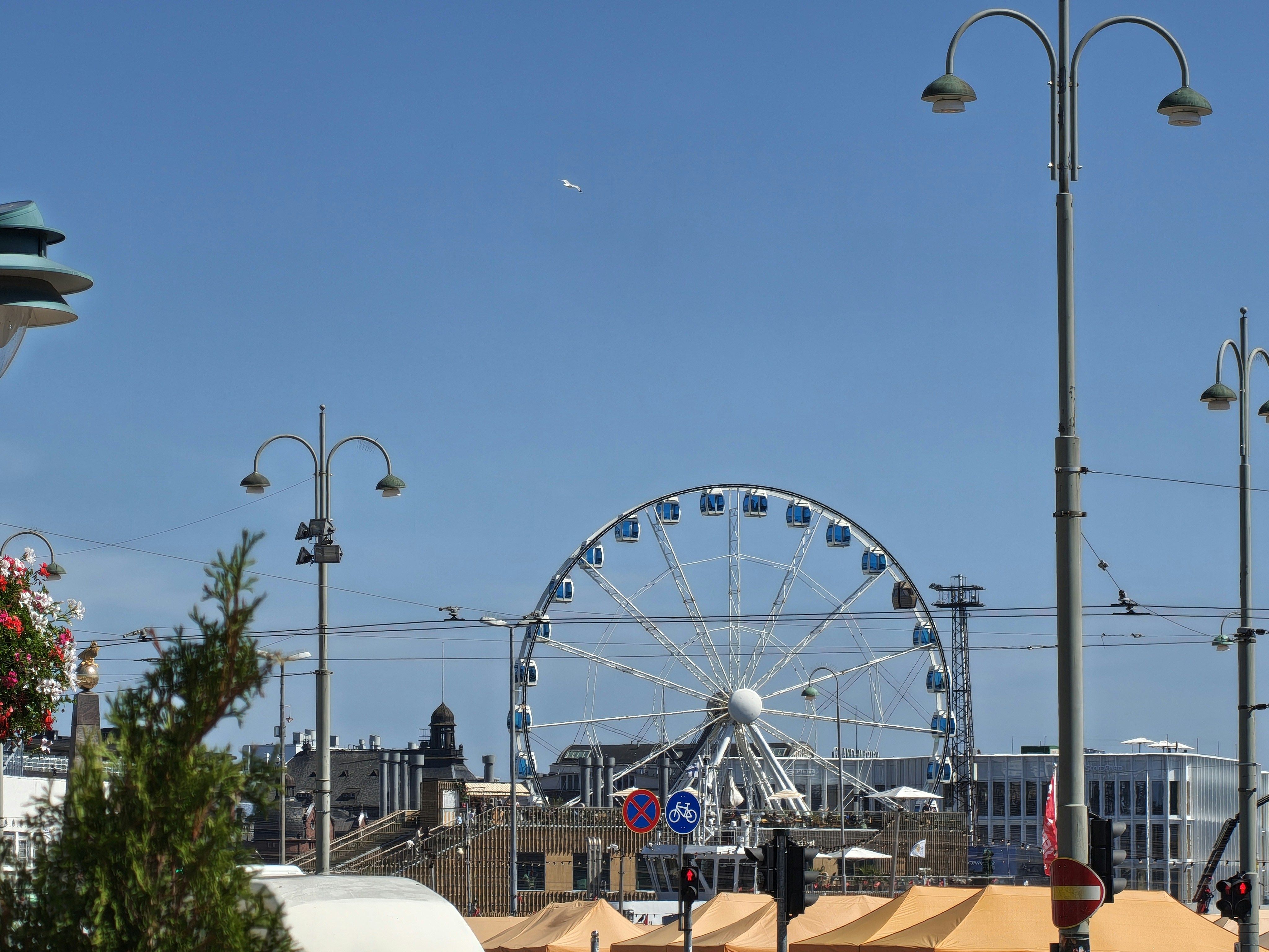 A large white ferris wheel against a clear blue sky above city streetlights