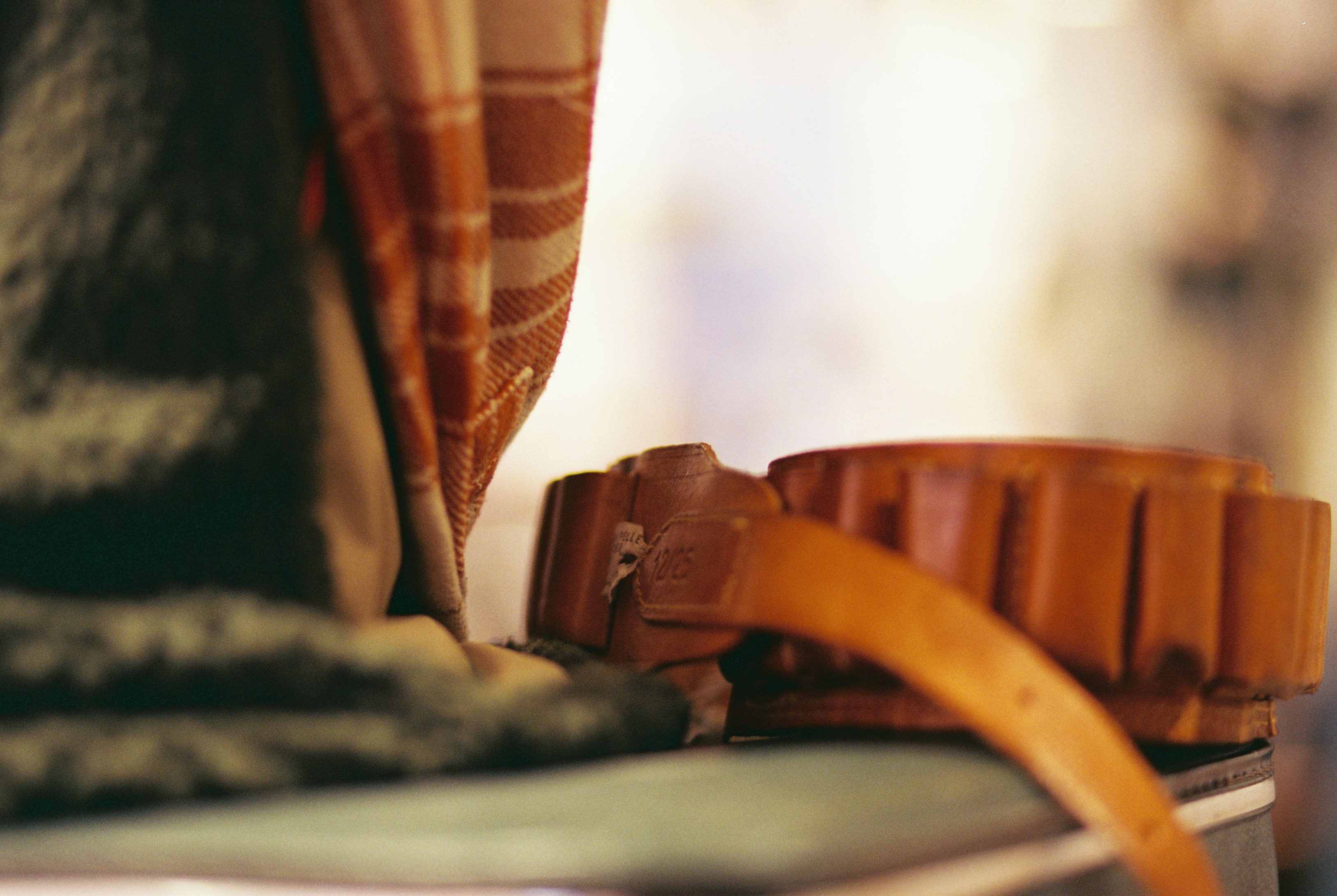 Close-up of a brown leather camera strap resting against dark fabric and a blurred background, highlighting texture and material detail. This is a still-life/physical product scene.