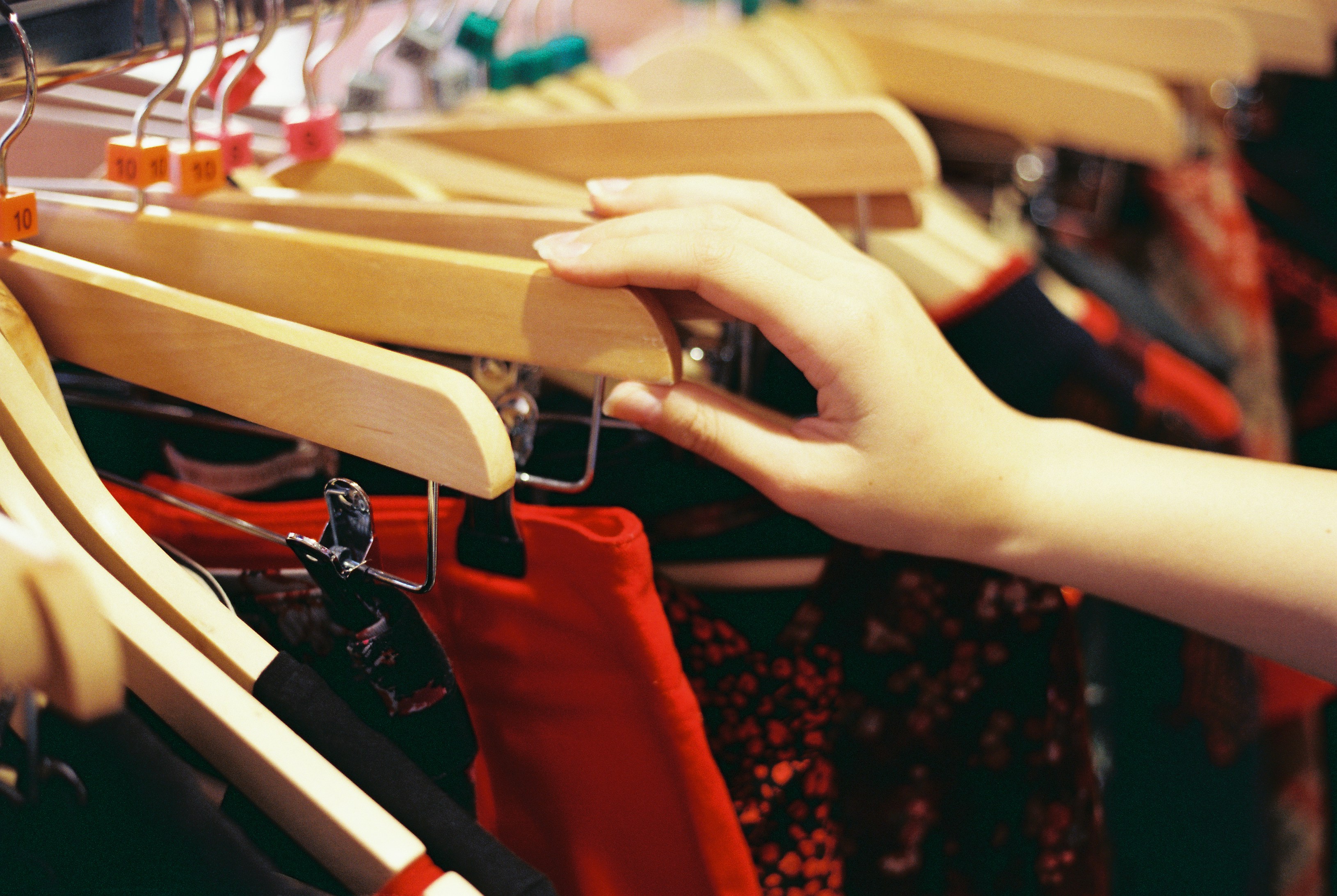 A hand reaches along a rail of wooden hangers to browse red patterned garments.