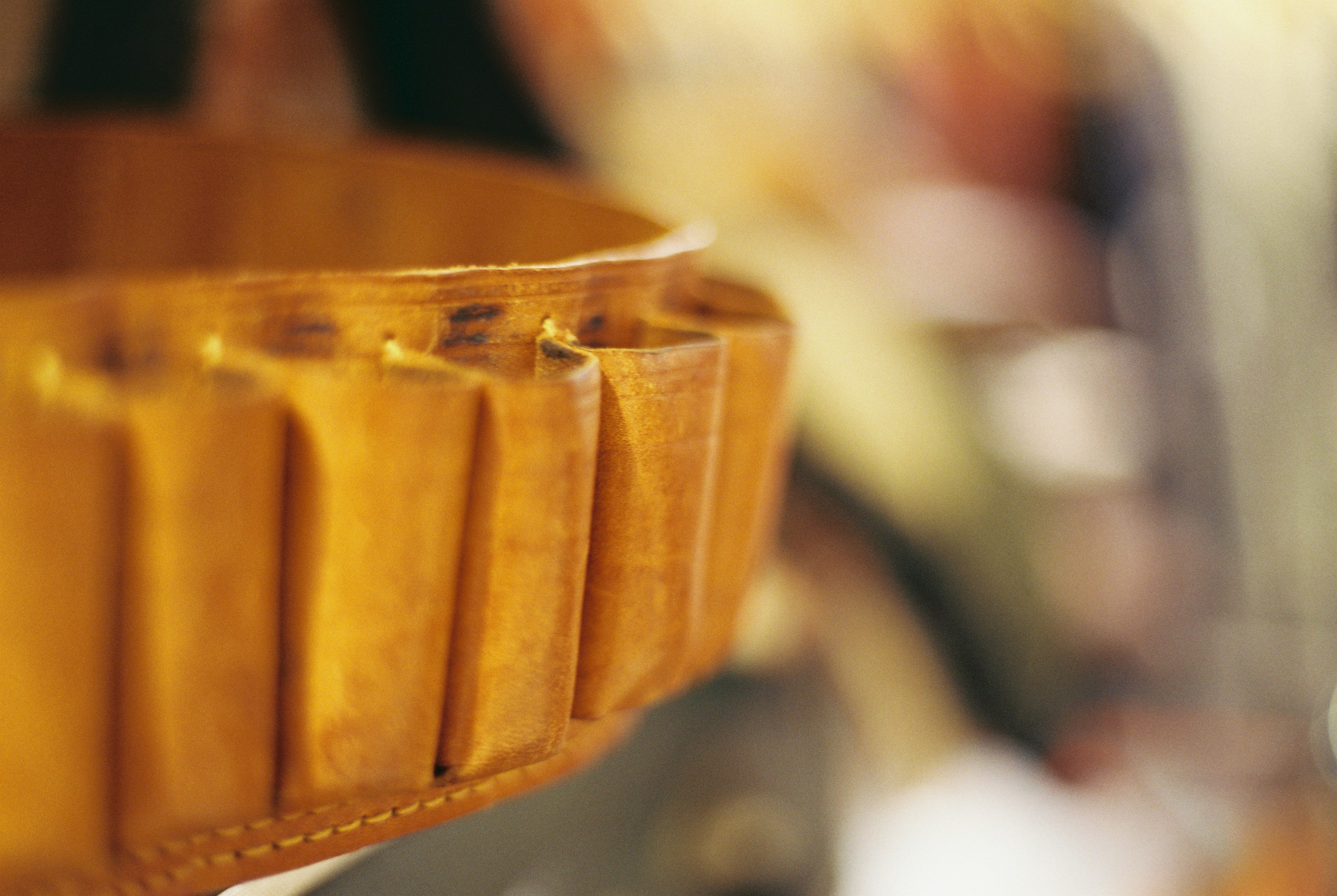 Close-up of a copper-toned, ribbed wooden or metal rim with stitching along the edge; shallow depth of field blurs the background, focusing on the texture and warm tones of the foreground element.