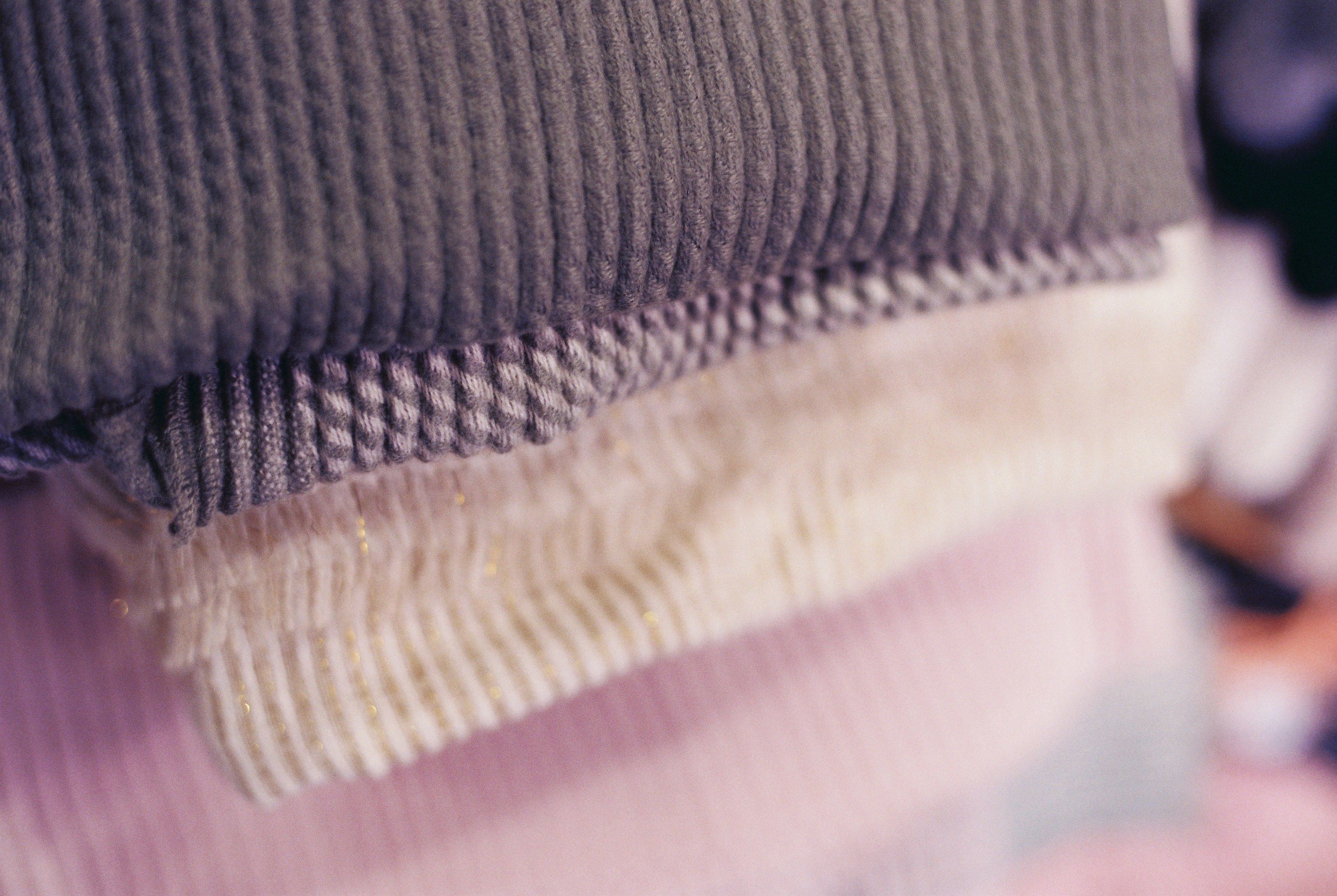 Close-up view reveals layered fabric textures and stitching along a seam. The image focuses on ribbed knit material above a frayed edge and soft fabric beneath, highlighting tactile detail and color gradients.