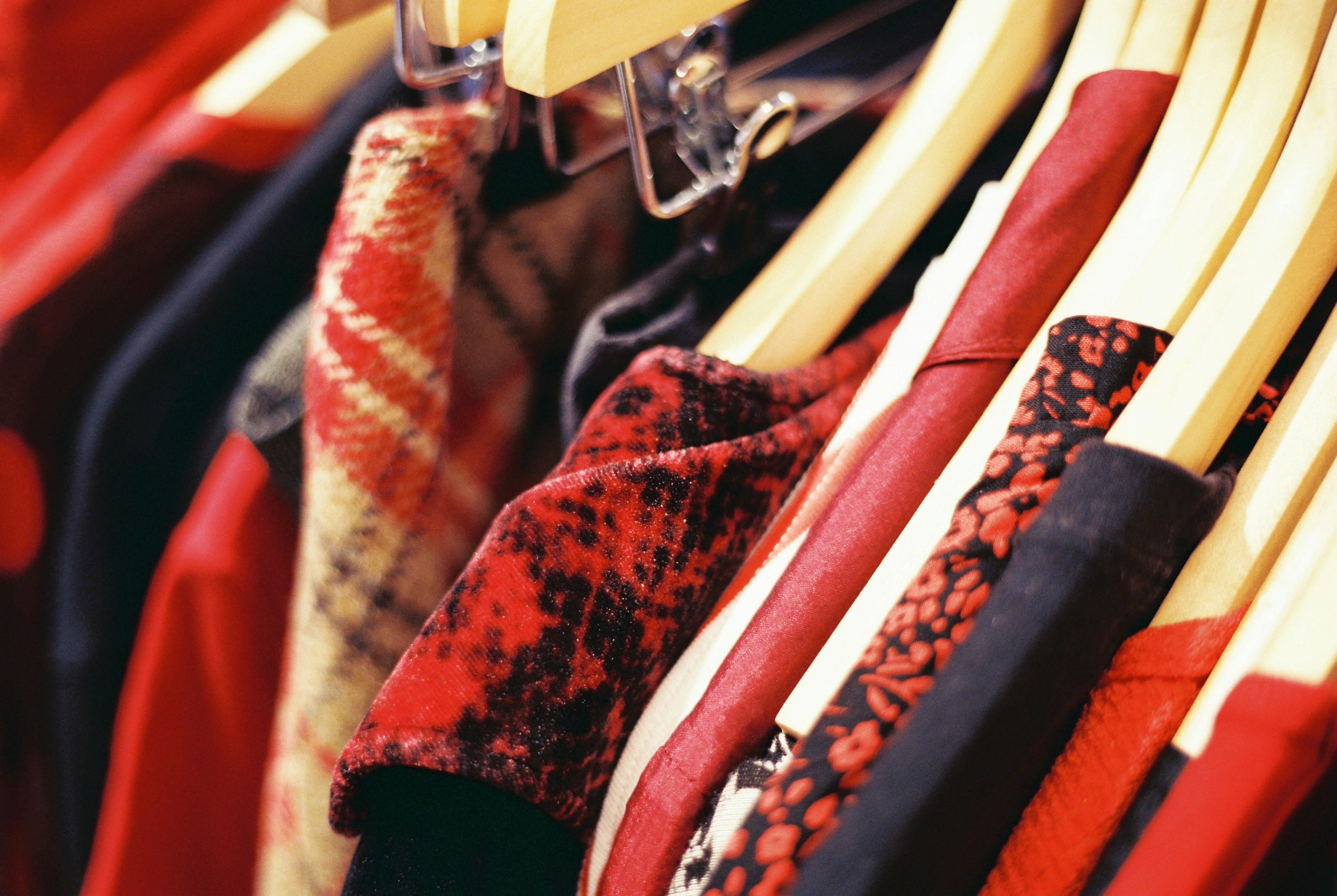 Rows of red and plaid fabrics hang on wooden hangers, forming a vivid textile display.
