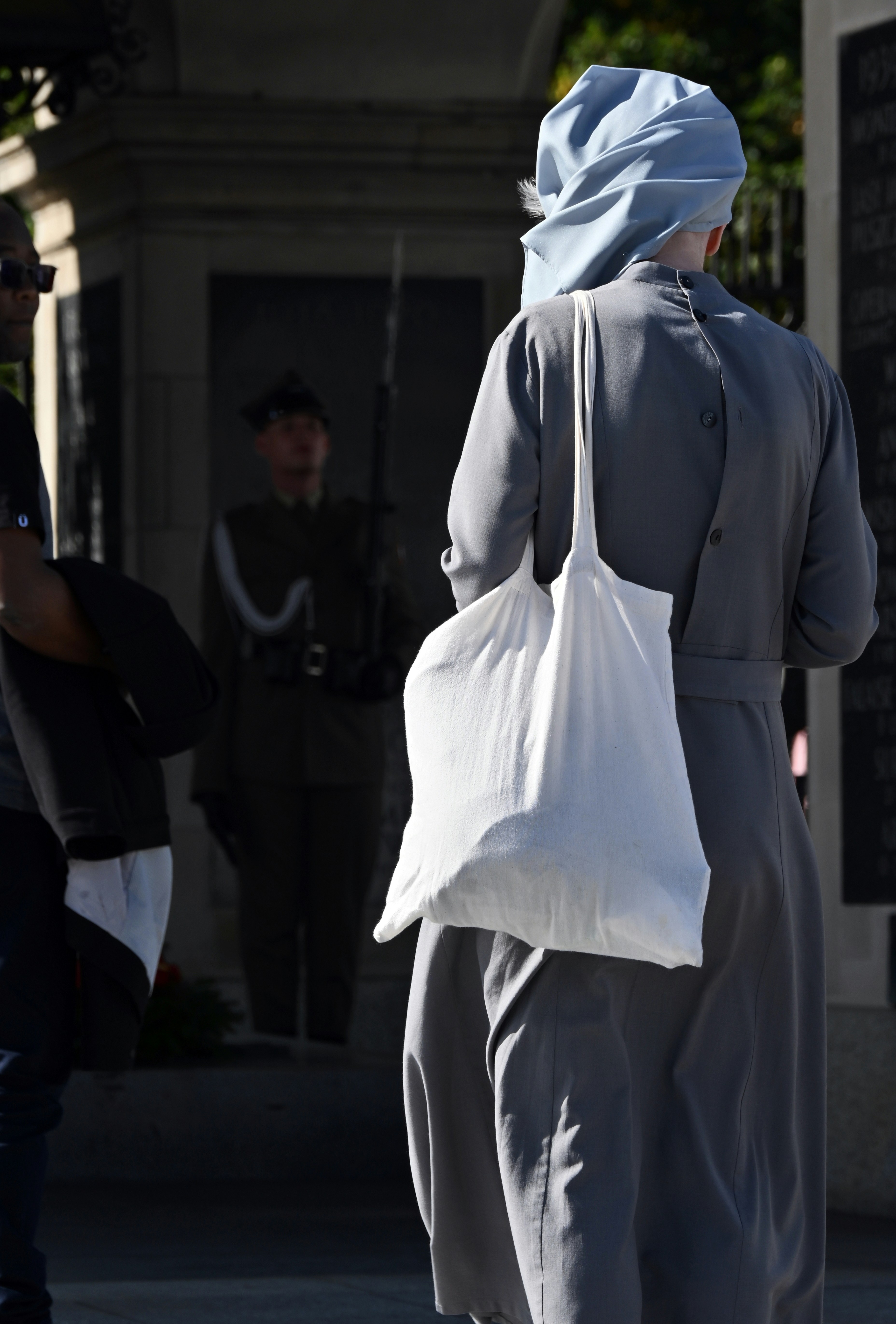 Quiet Strength in Grey: A Woman with a White Tote Near a Guarded Entrance