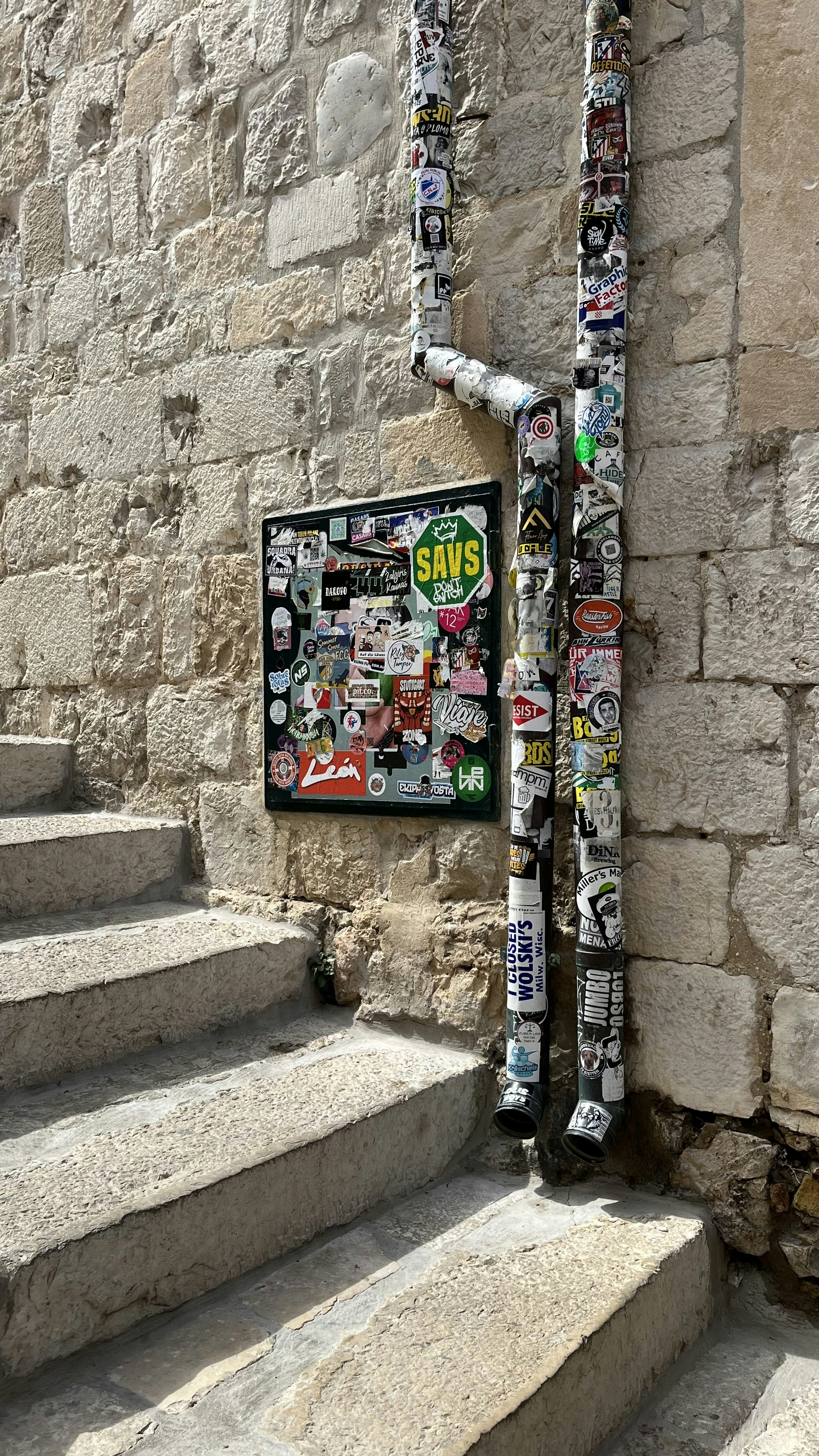 Stickered pipes by a sunlit stone stairwell