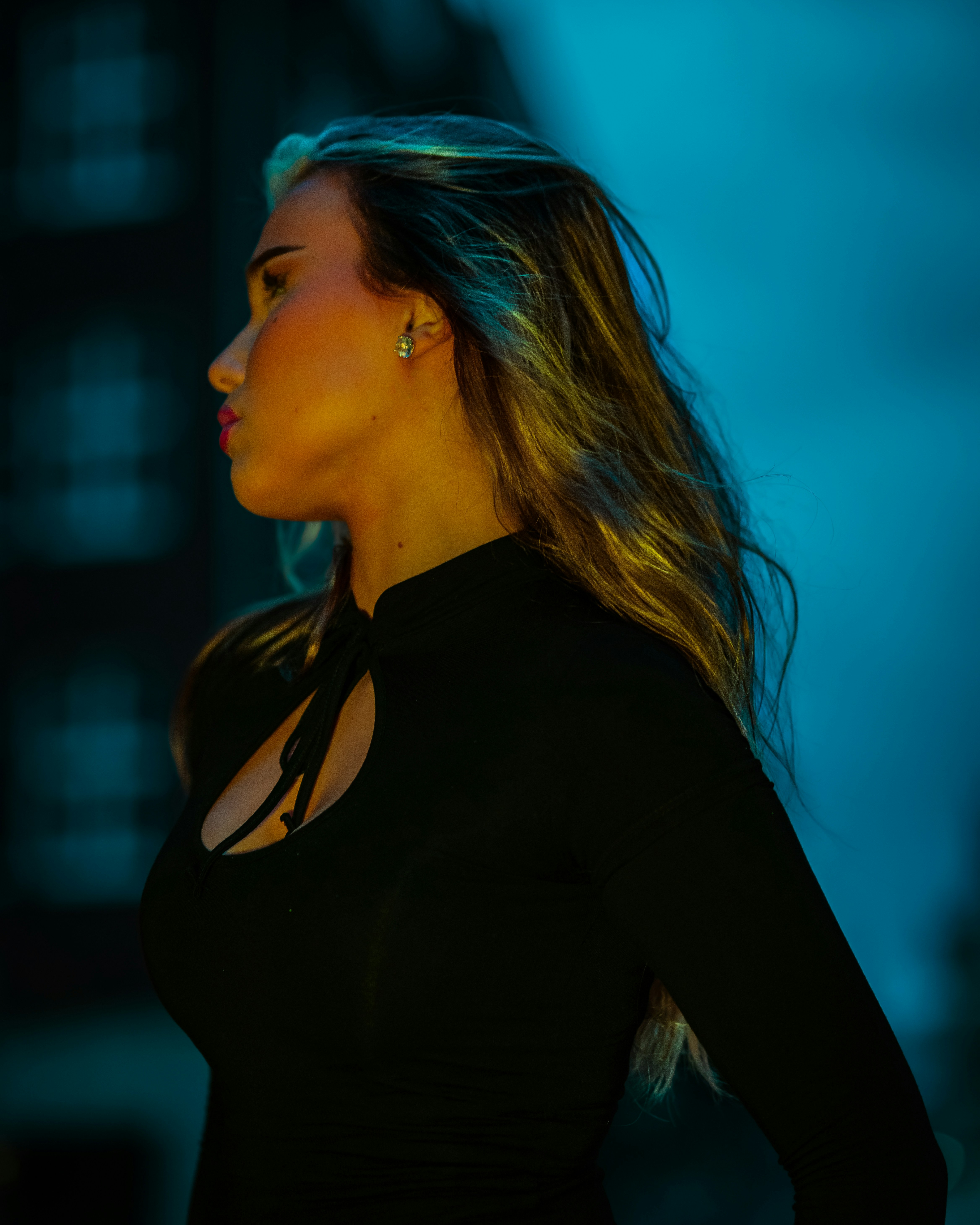 Female subject in profile, illuminated with blue-green ambient light; close-up from shoulders up, wearing a black top with a cut-out neckline. A logo-free, candid portrait suitable for editorial use.