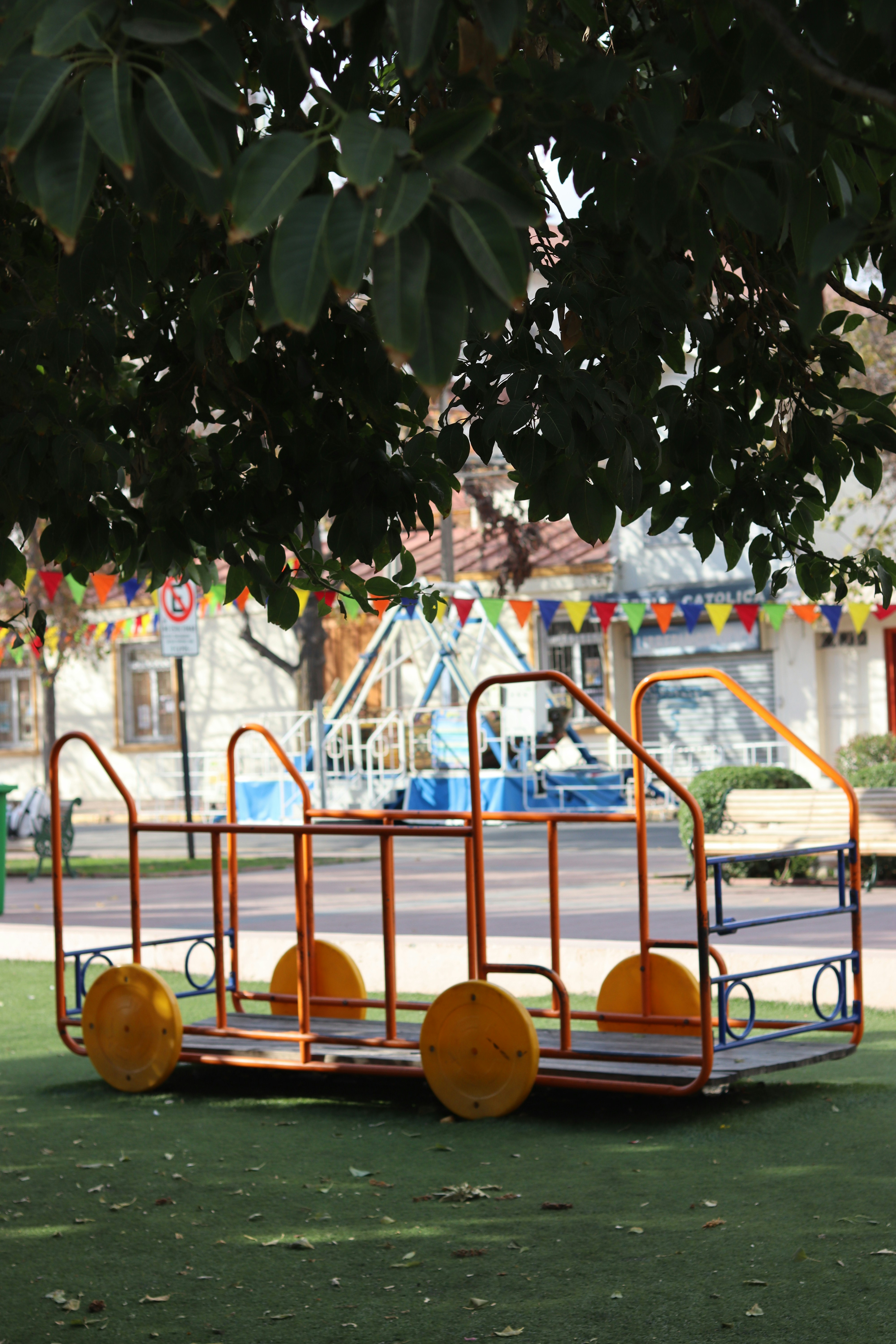 An orange metal play train carriage on a green lawn with colorful bunting