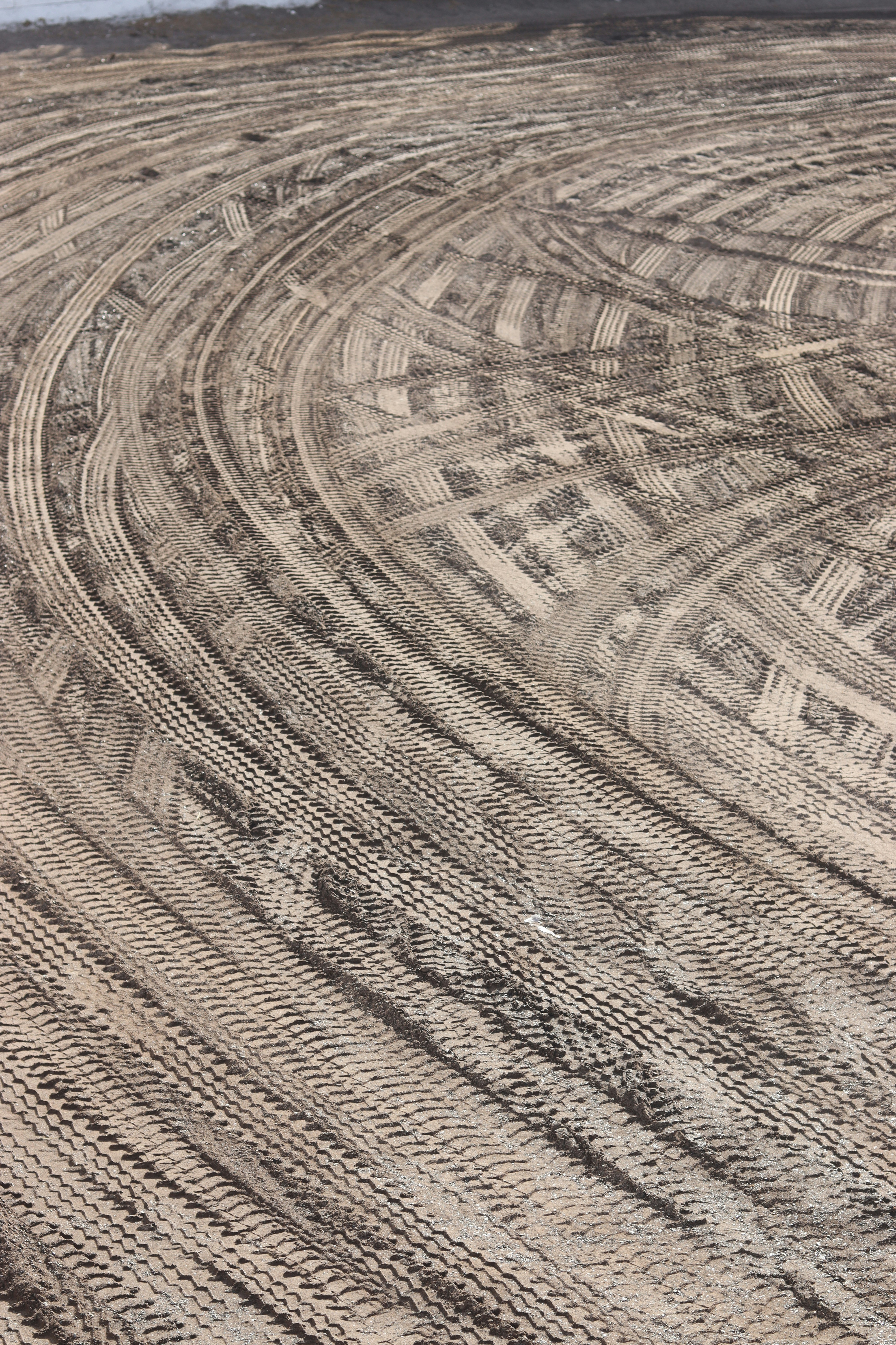 Tire tread imprints sketch concentric patterns across sandy surface