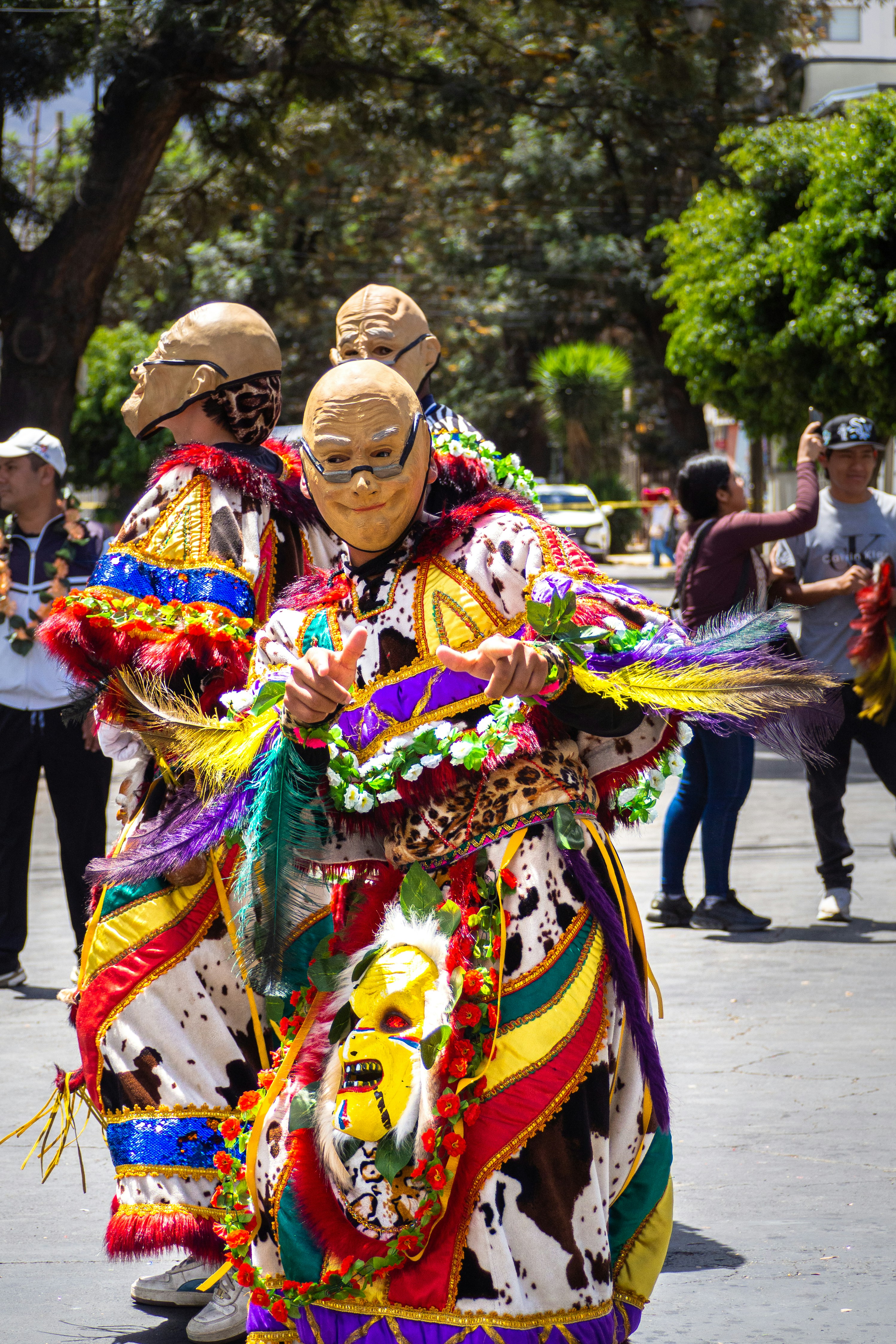 Vibrant costumed performers with ornate masks and feathered accessories in a lively street scene during a festival.