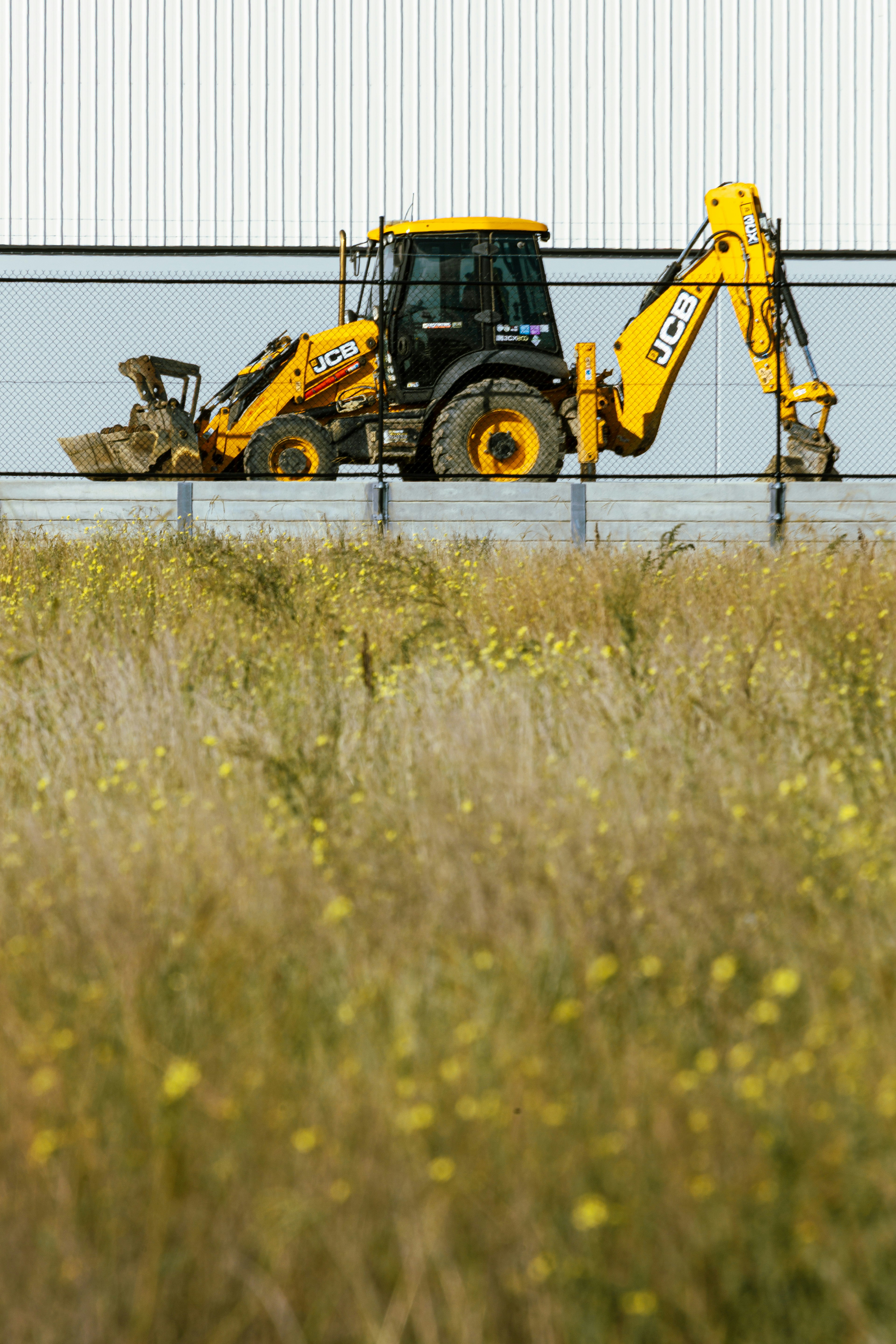 Midfield JCB: A Yellow Excavator Paused at the Fence