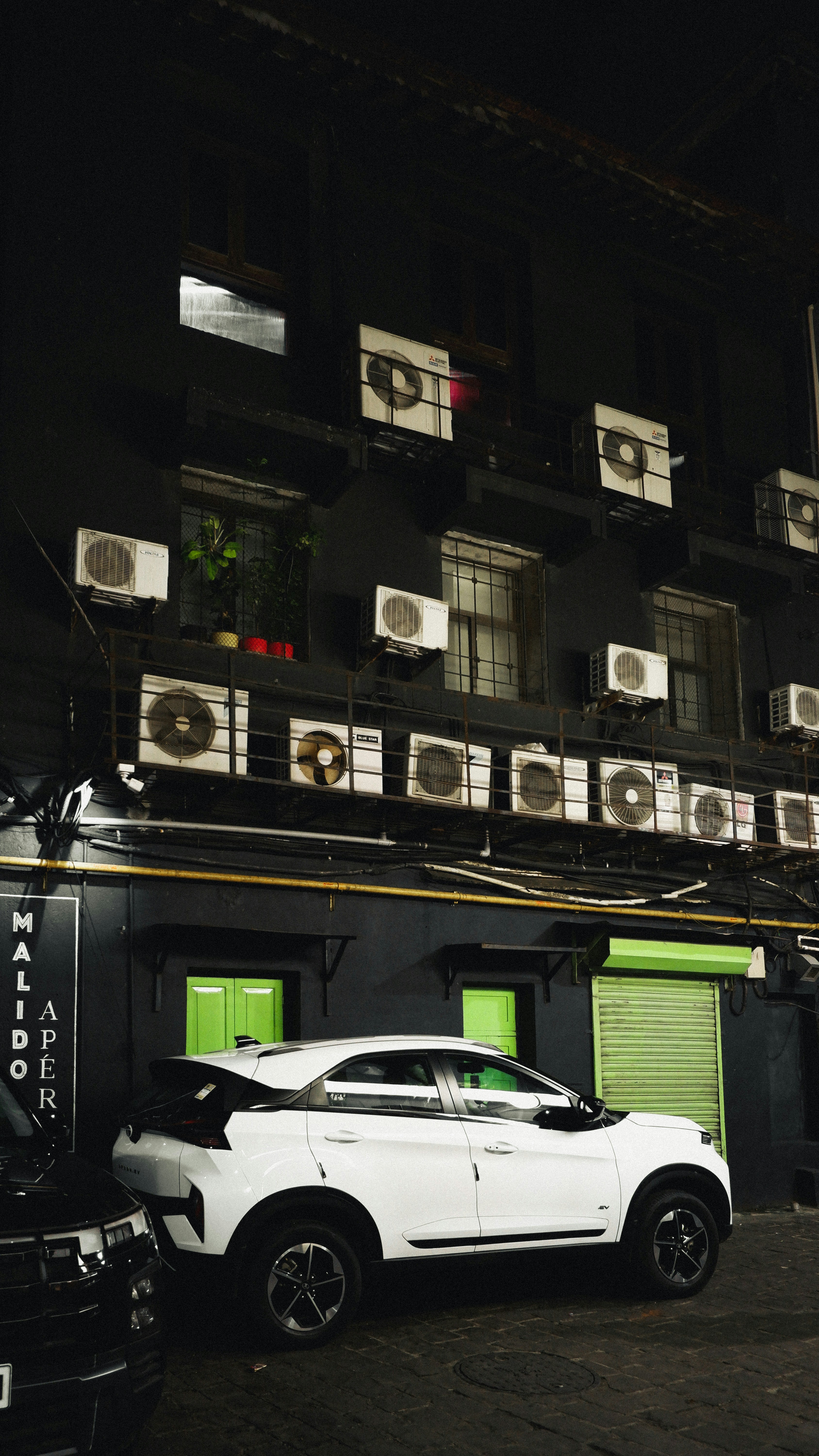 White SUV under a wall of city HVAC units at night