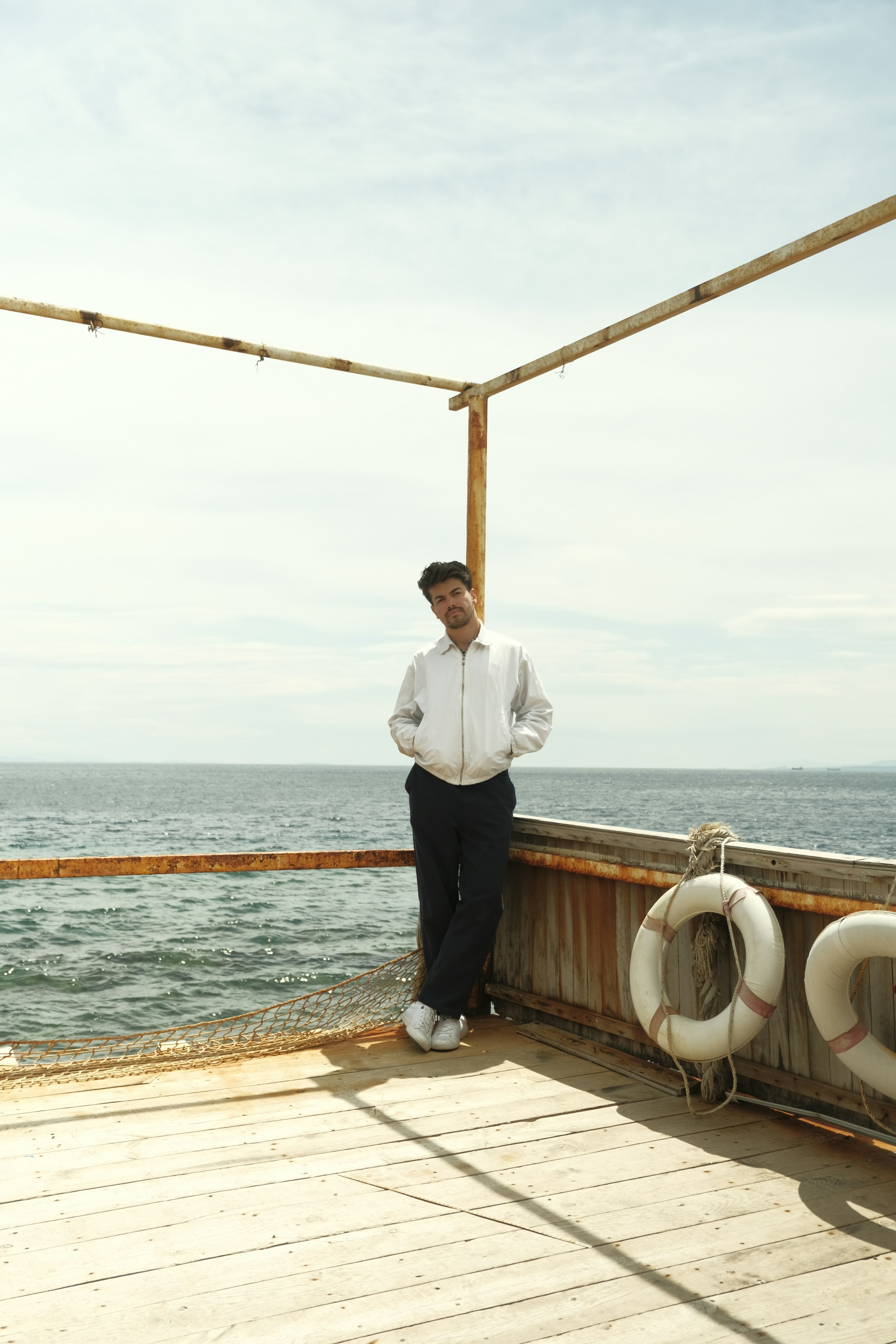 Man in white shirt leaning on a weathered railing against sea backdrop