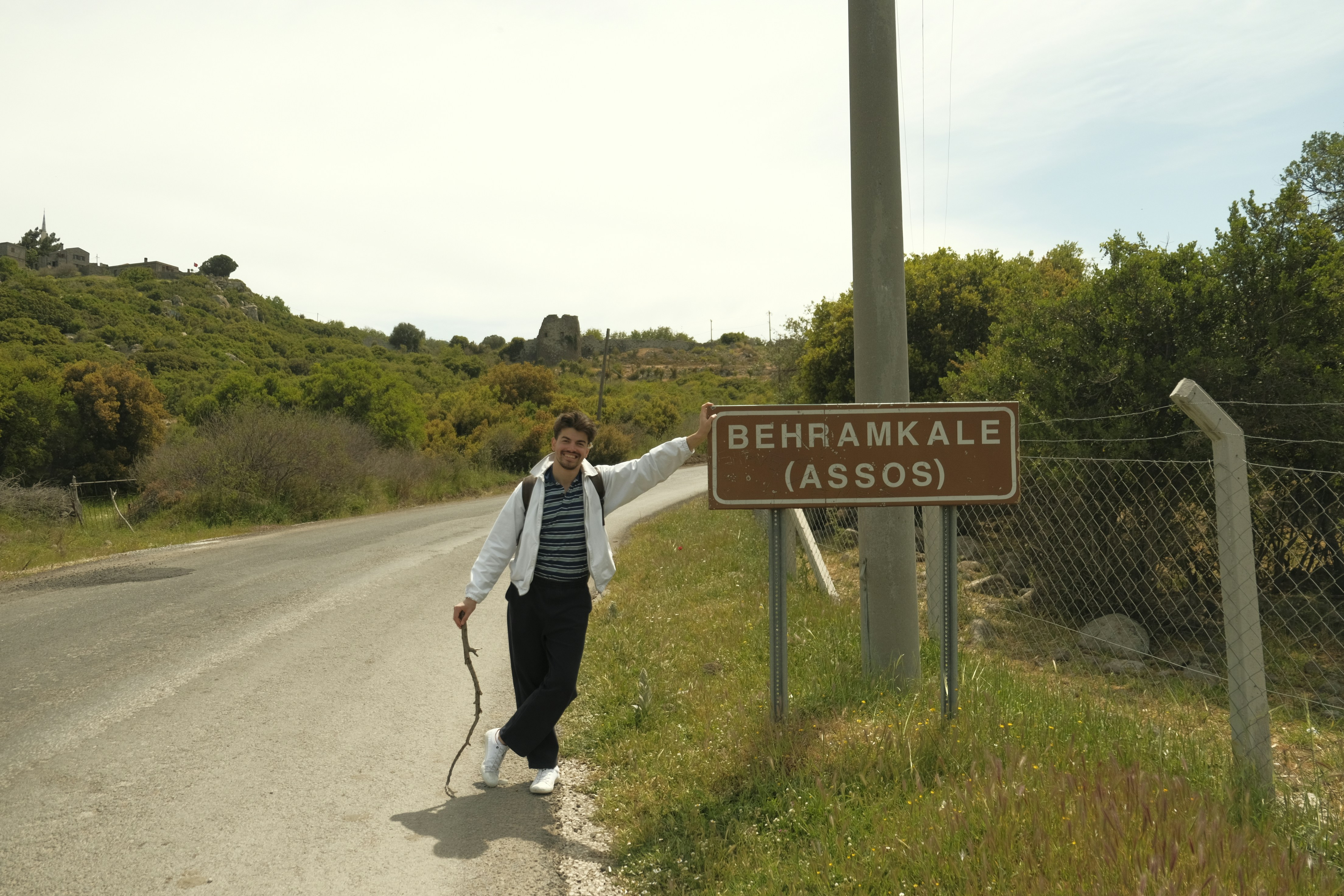 Person in white jacket posing beside a rural road sign