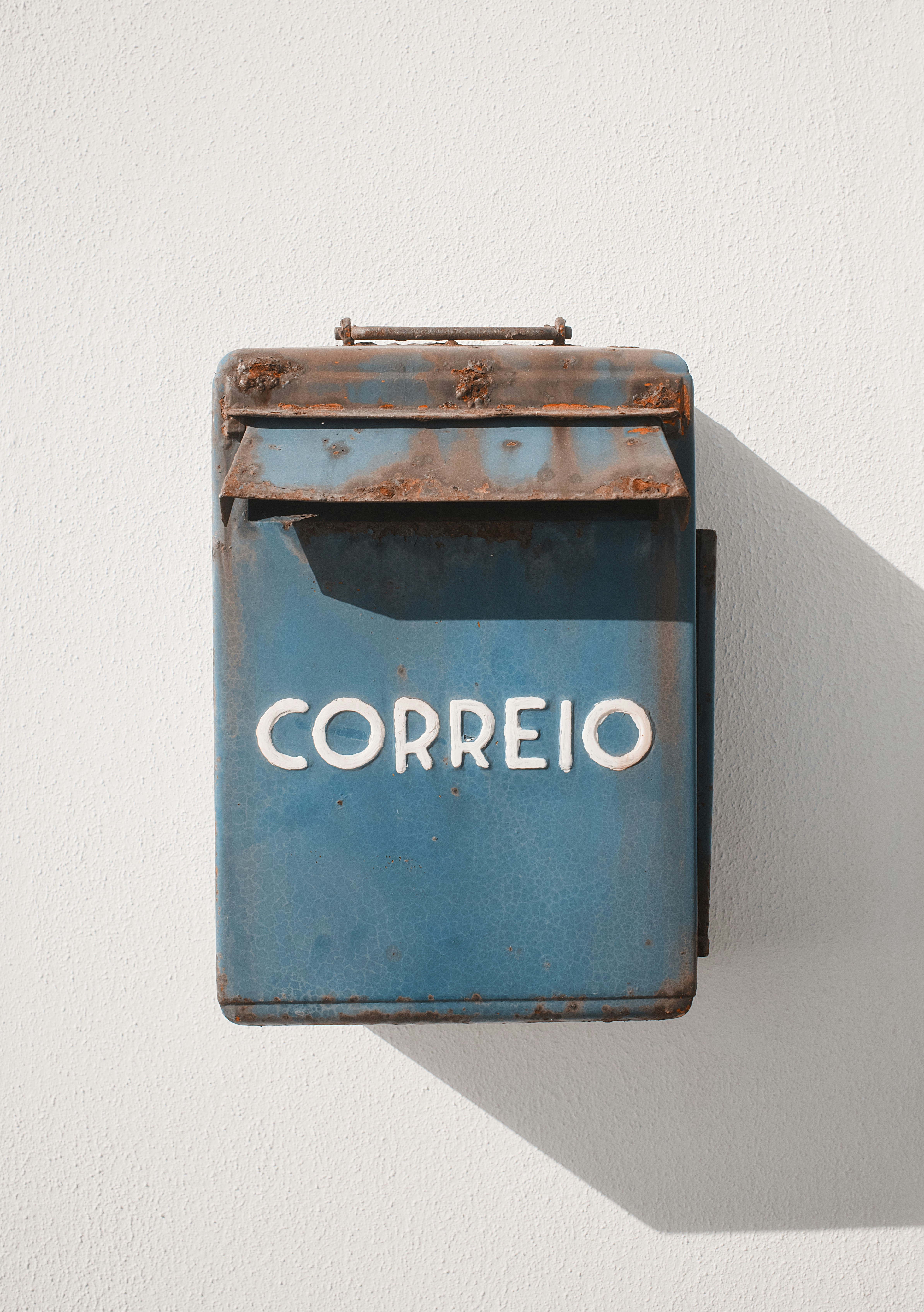 A weathered blue metal mailbox with the word CORREIO on a white wall