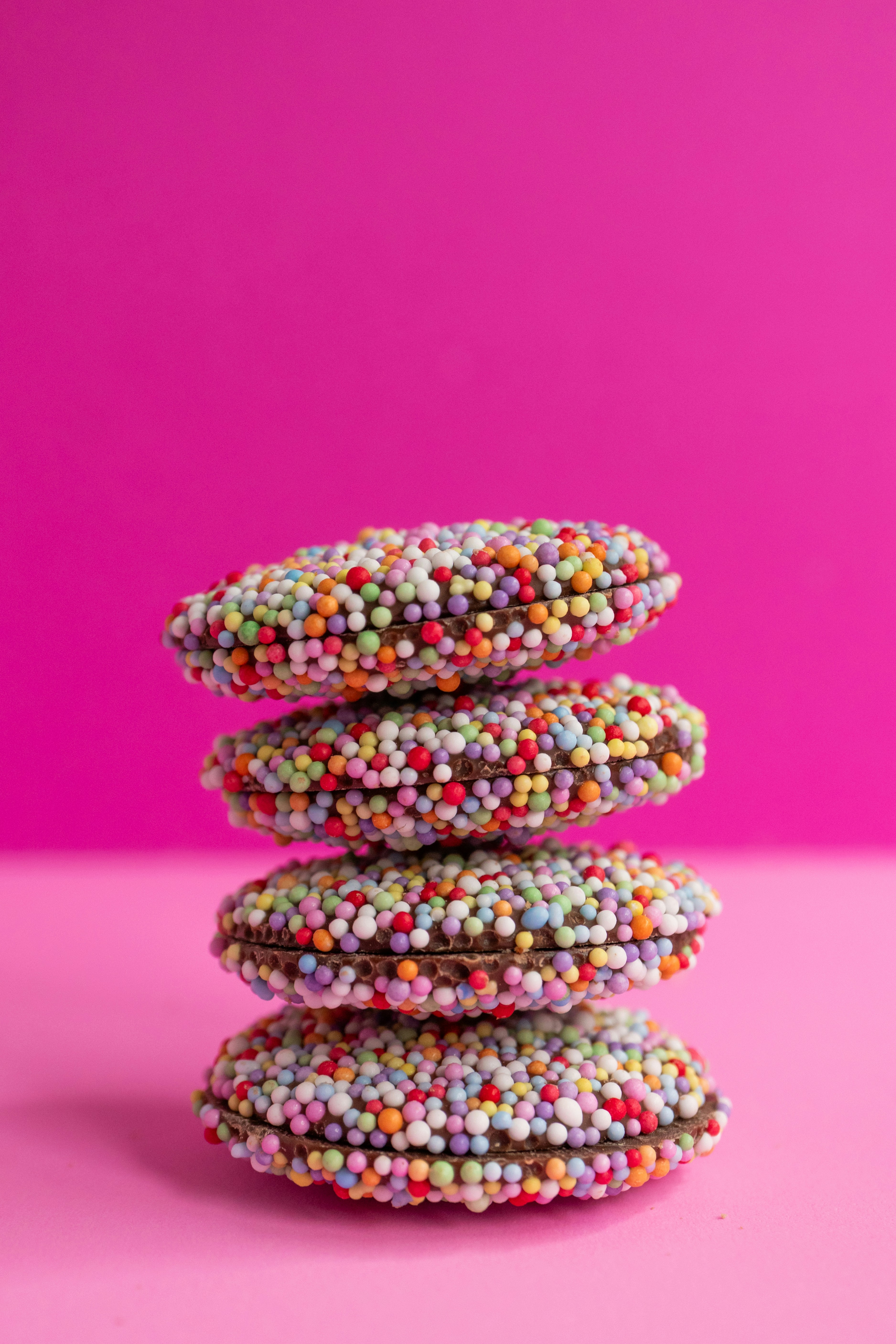 Stack of Candy-Sprinkled Donuts Against a Neon Pink Backdrop