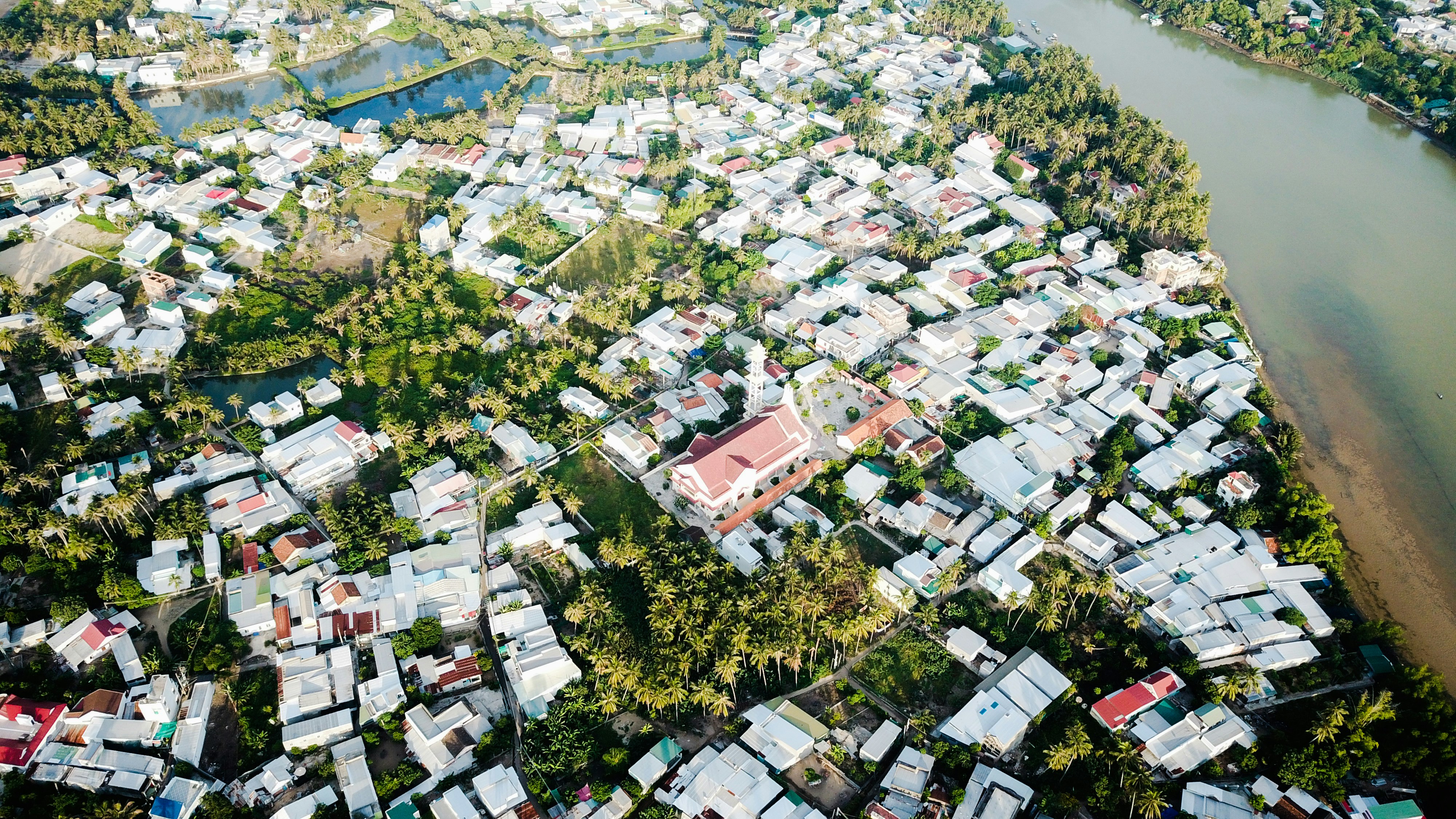 Aerial Pulse: Riverside Village Nestled Among Red-Roofed Houses