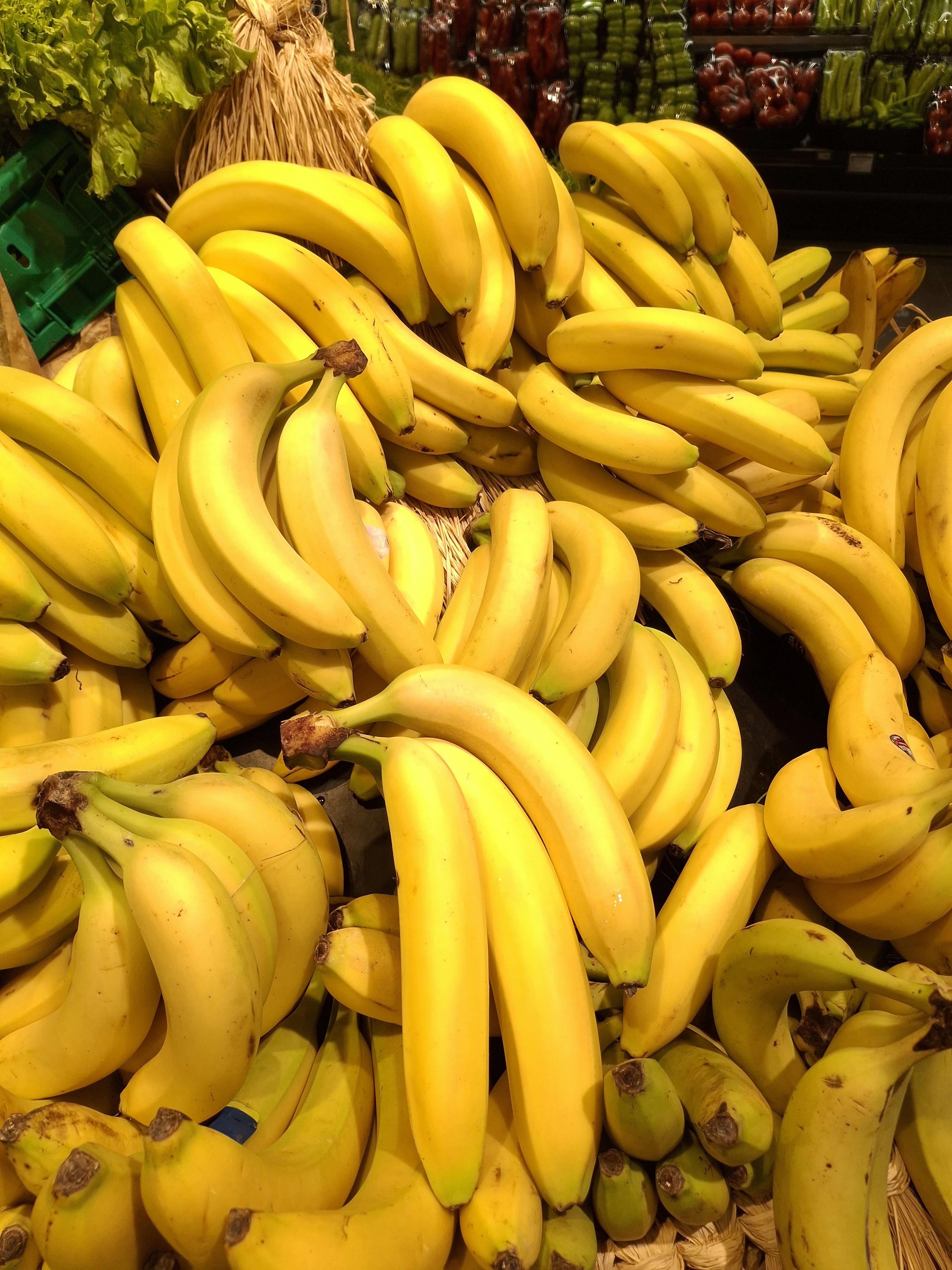 Bright yellow bananas piled high on a market display, highlighting their curved shapes and vibrant color. A still-life of fresh fruit in a grocery setting.