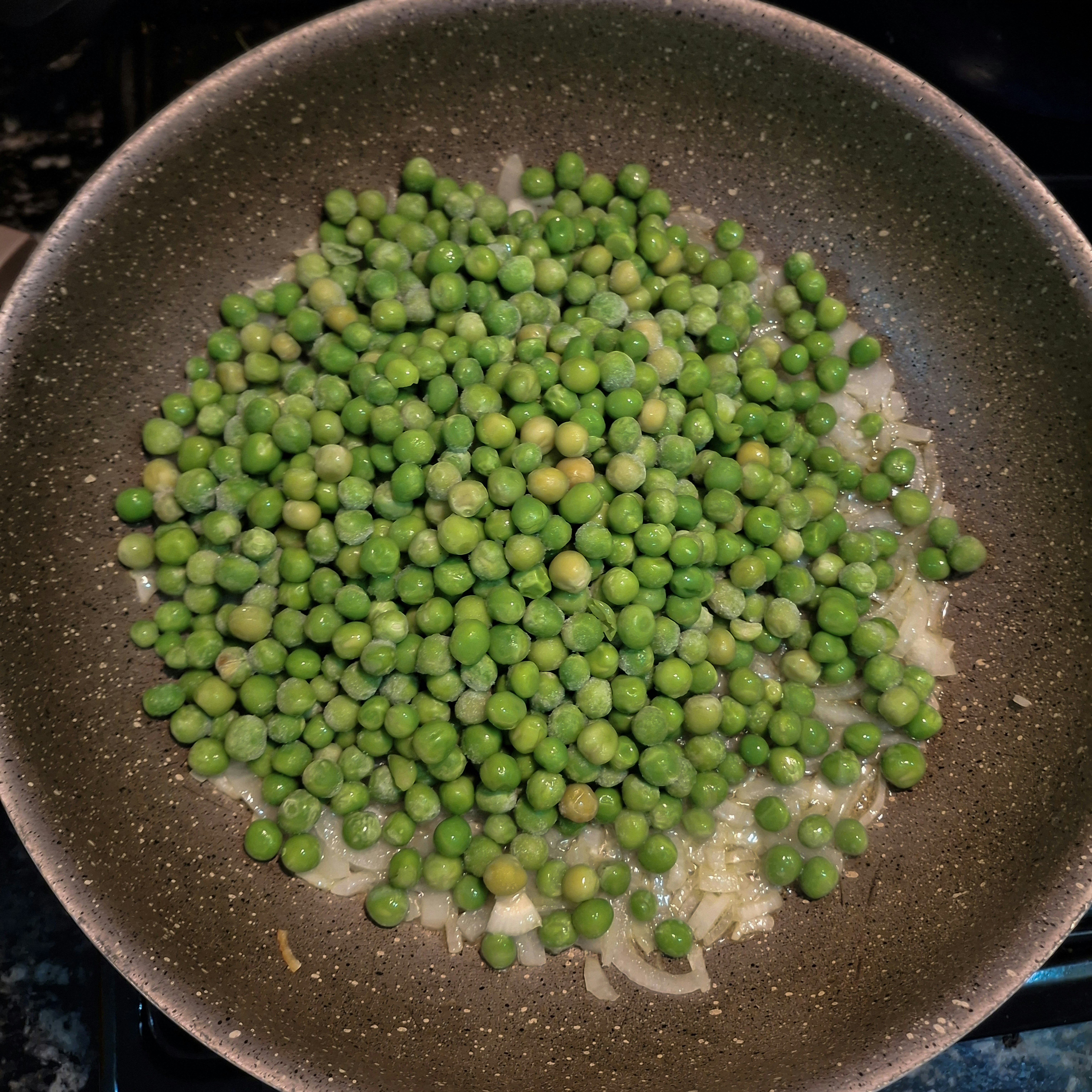 Bright green peas mingle with sizzling onions in a seasoned skillet, capturing a close-up of the cooking process.