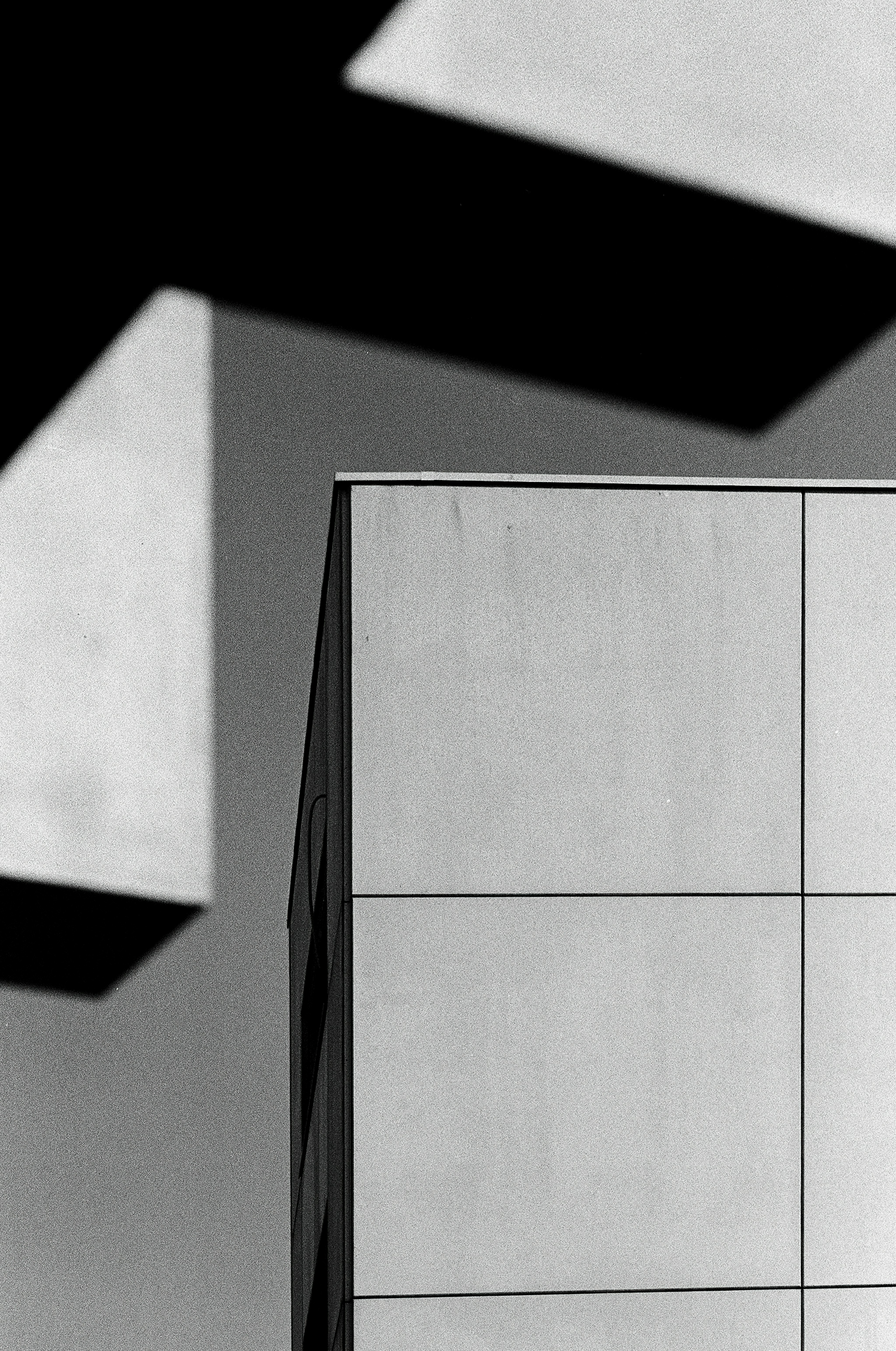 Sharp graphic shadow cutting across a minimalist building facade with a grid pattern, black and white film photography.