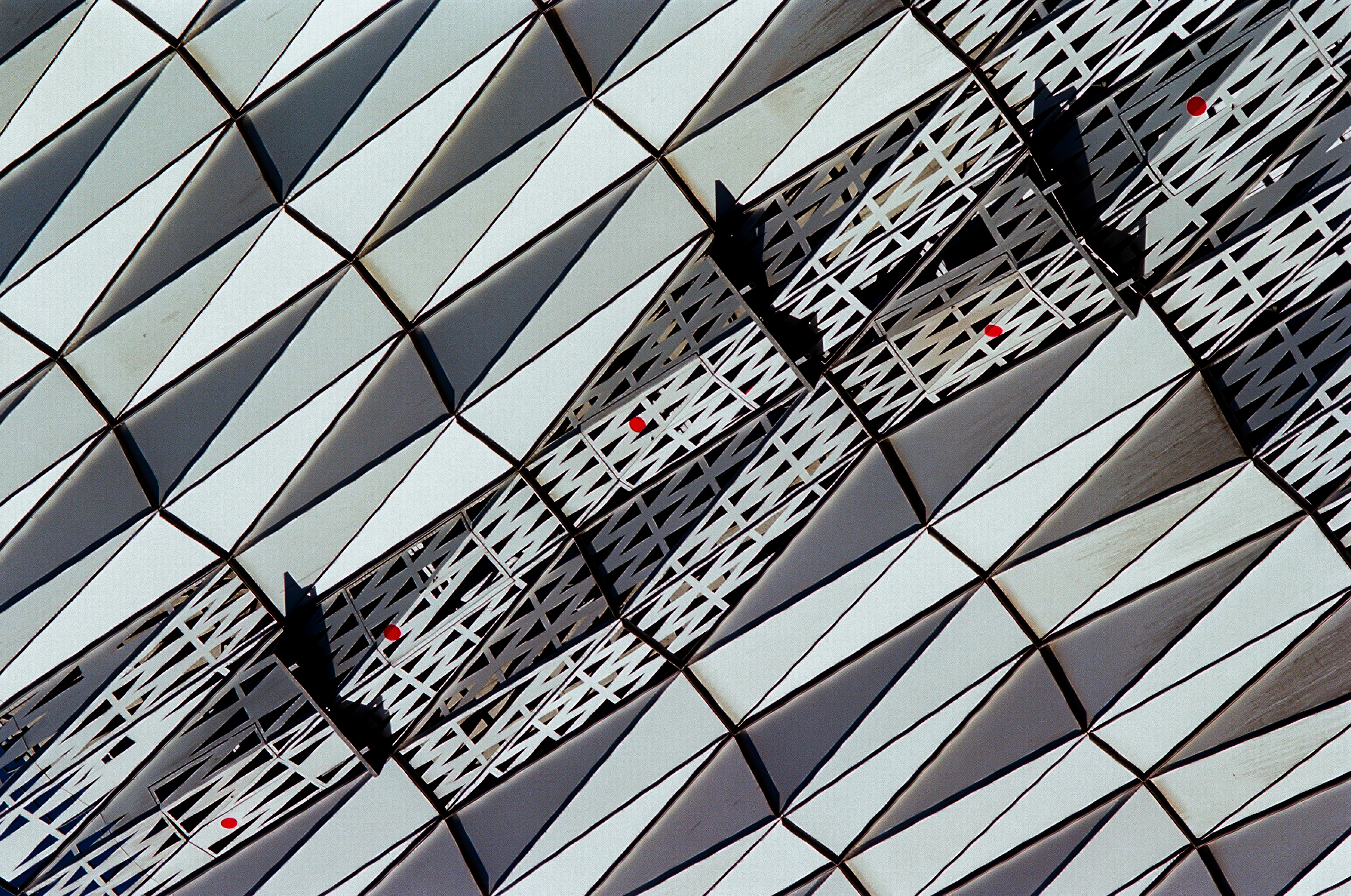 Triangulated metallic facade pattern with small red accent details, diagonal composition, color film photography.