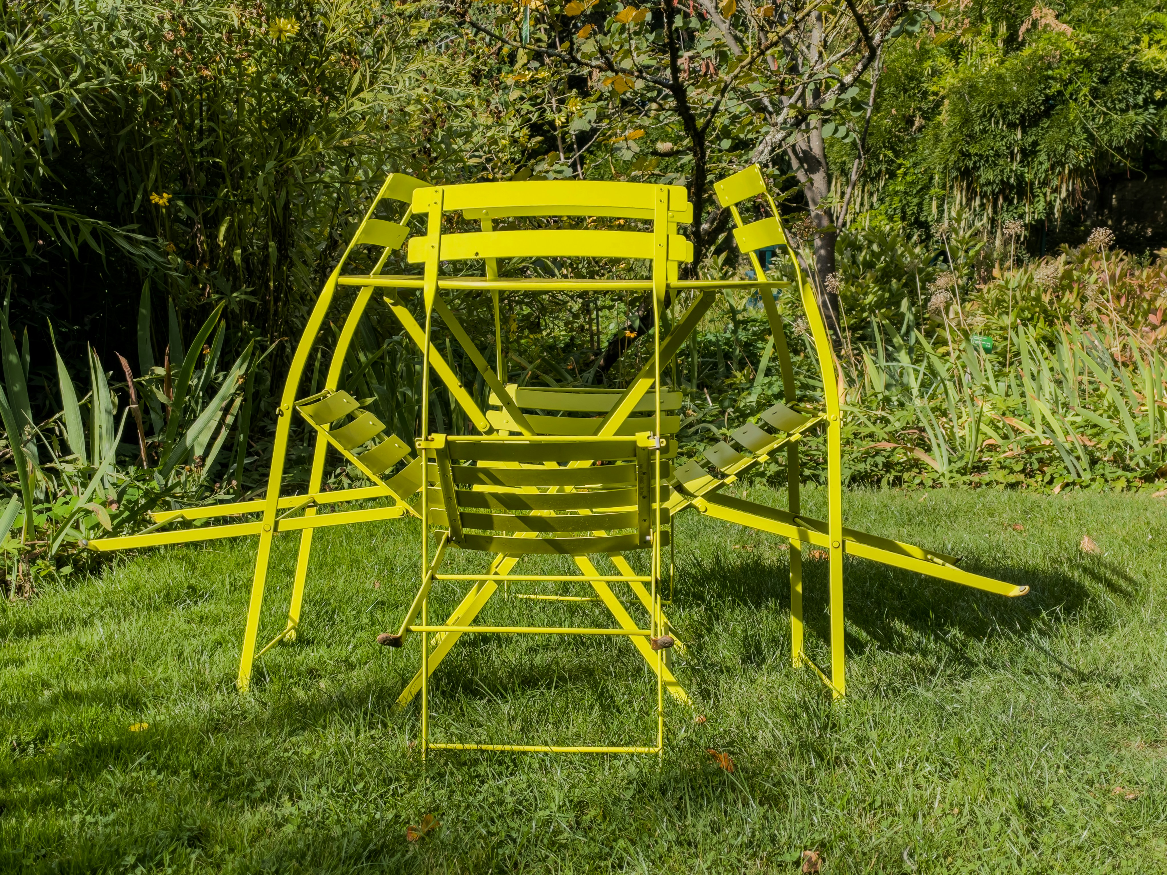 Four lime green metal chairs stacked together on a lush green lawn