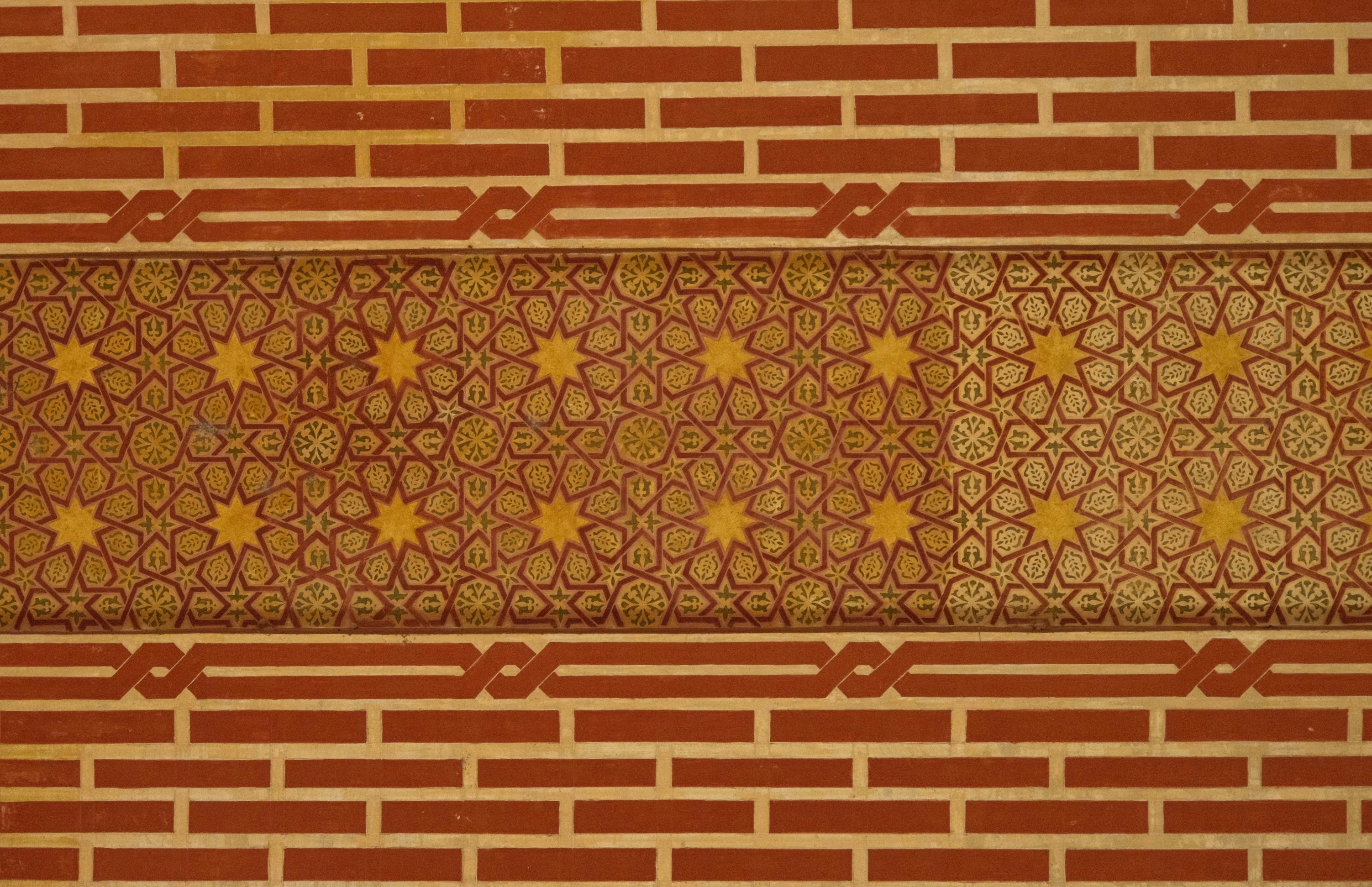 Decorative brick band with alternating linear bricks and a central patterned motif, creating a horizontal stripe across a wall. The motif appears to be a repeating circular star-like design, suggesting a decorative frieze rather than a functional surface.