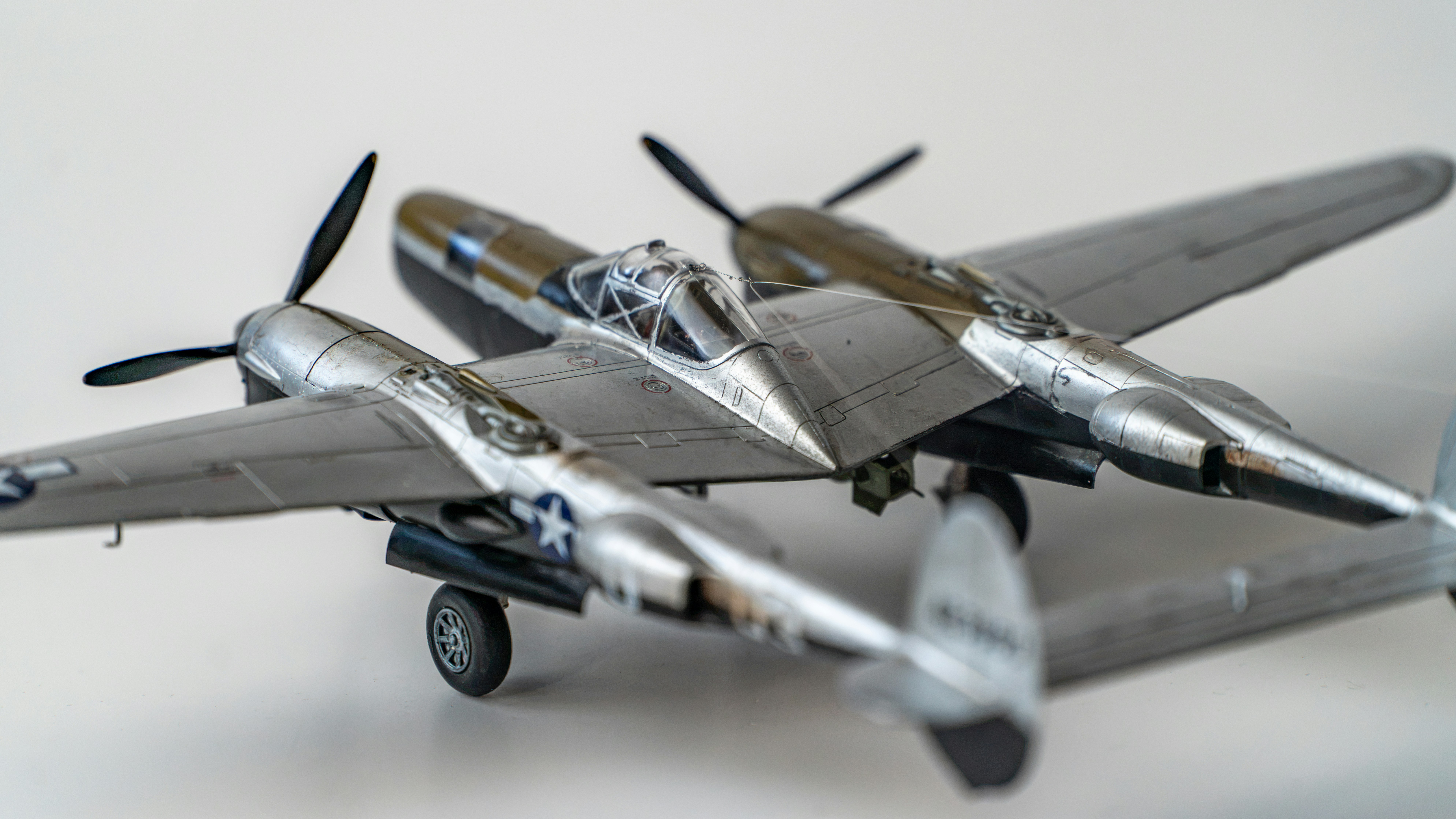 Close-up of a metallic twin-engine aircraft model with detailed cockpit and propellers, set against a soft neutral backdrop.