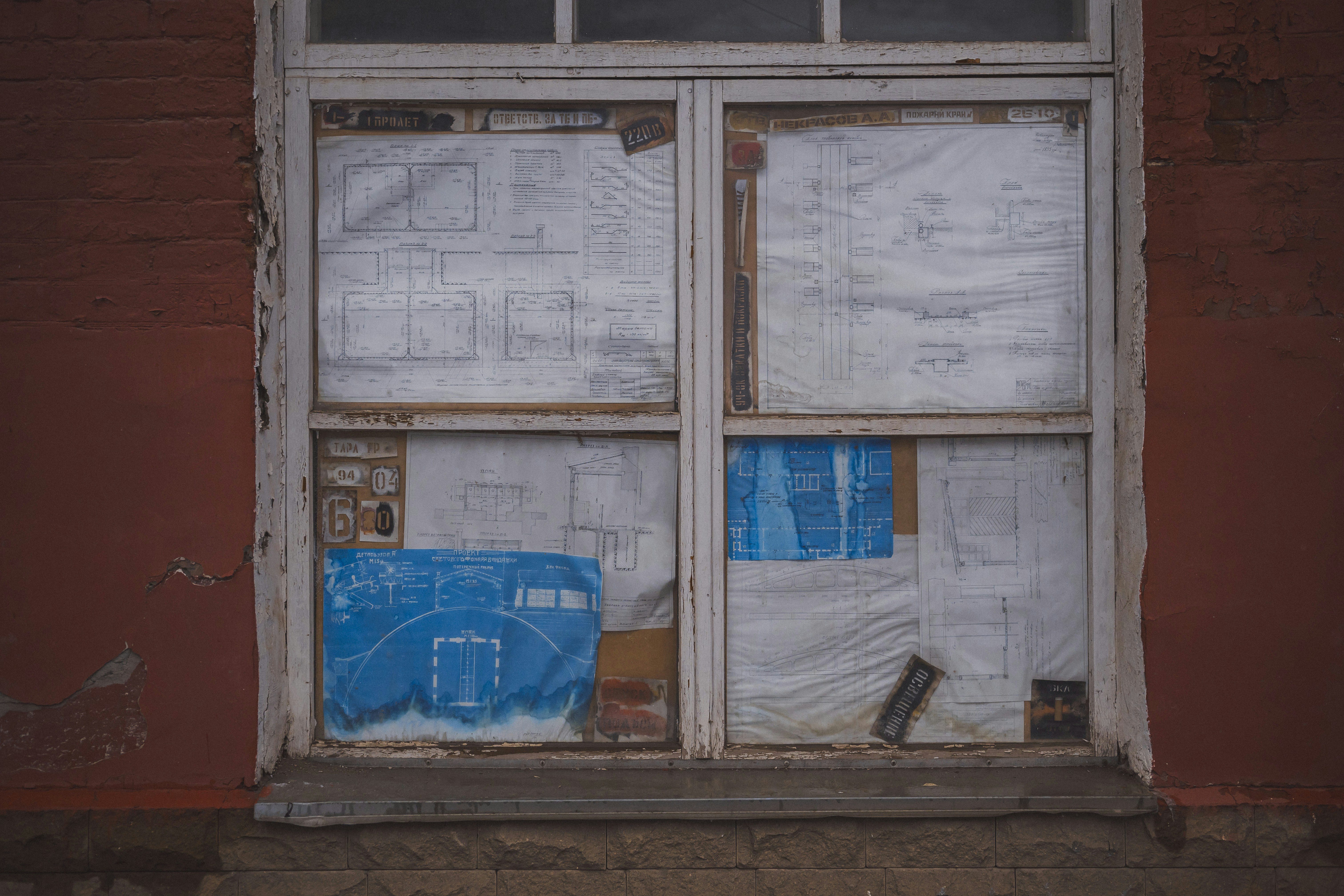 Weathered Window Ledger: Blue Tarpaulins Beneath a Fractured Glass
