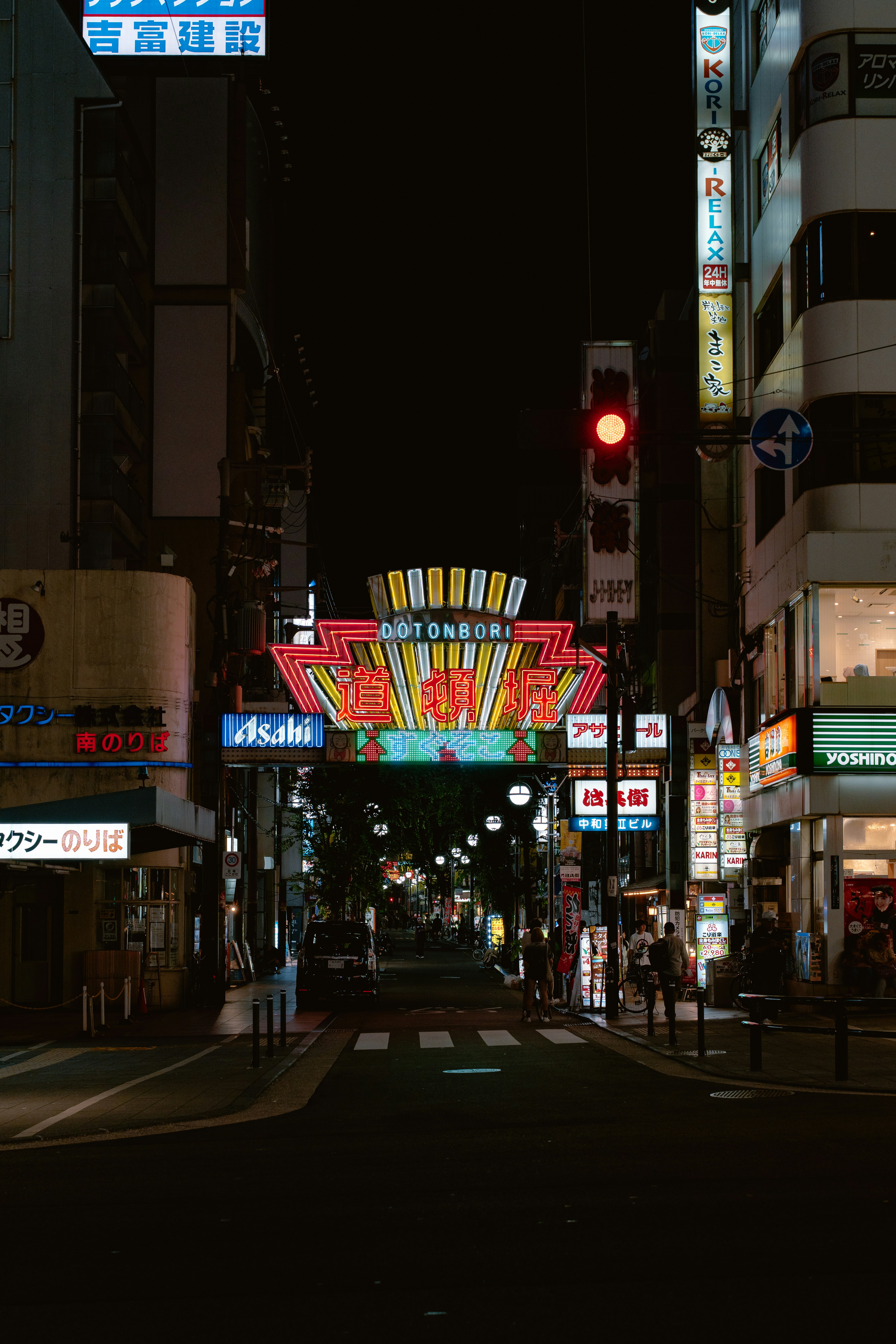 Brightly lit Dotonbori archway at night guides the eye down a bustling street lined with illuminated signs and storefronts.