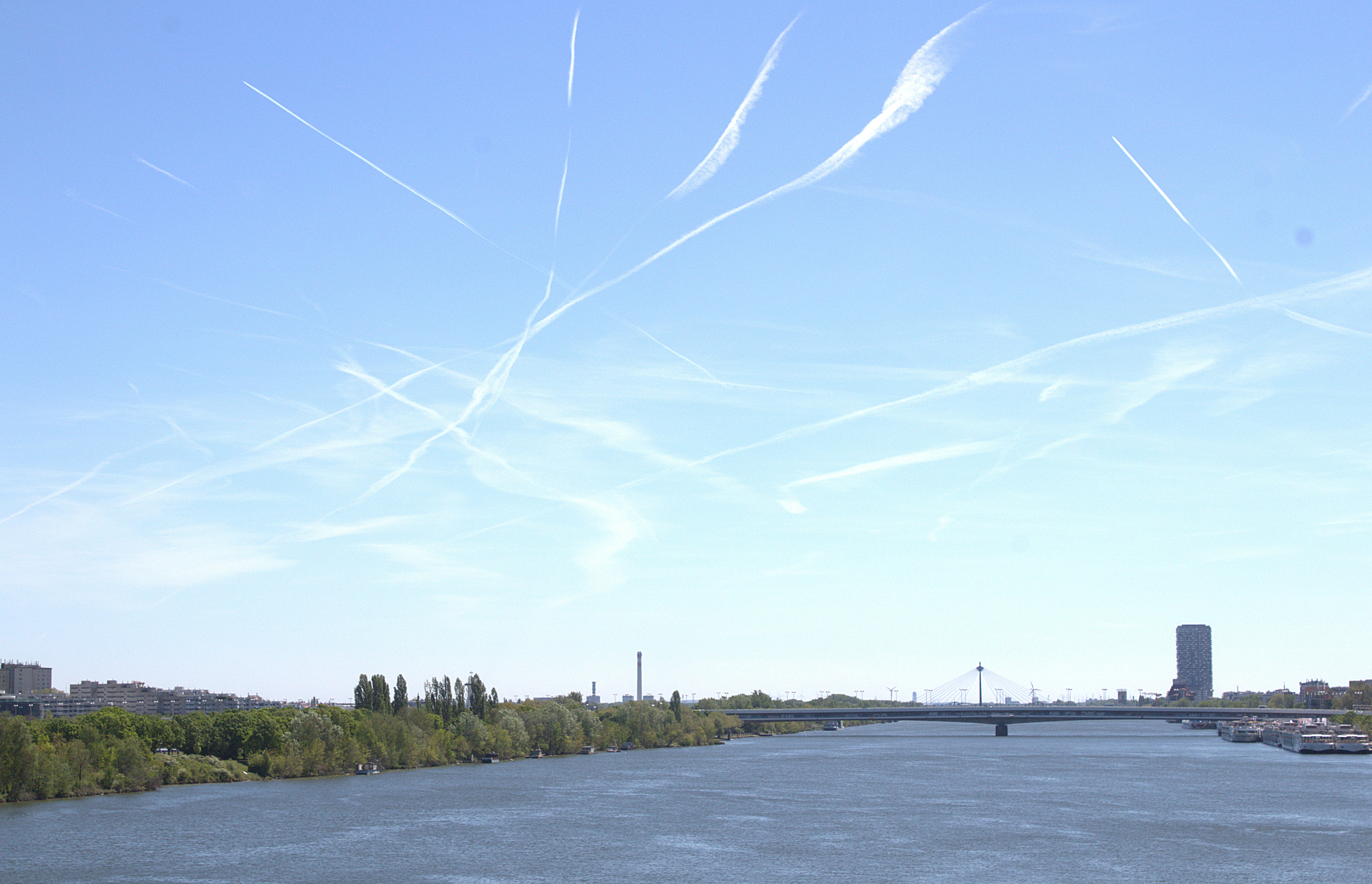 River amid Contrails: A Quiet Cityscape Under Expanding Skies