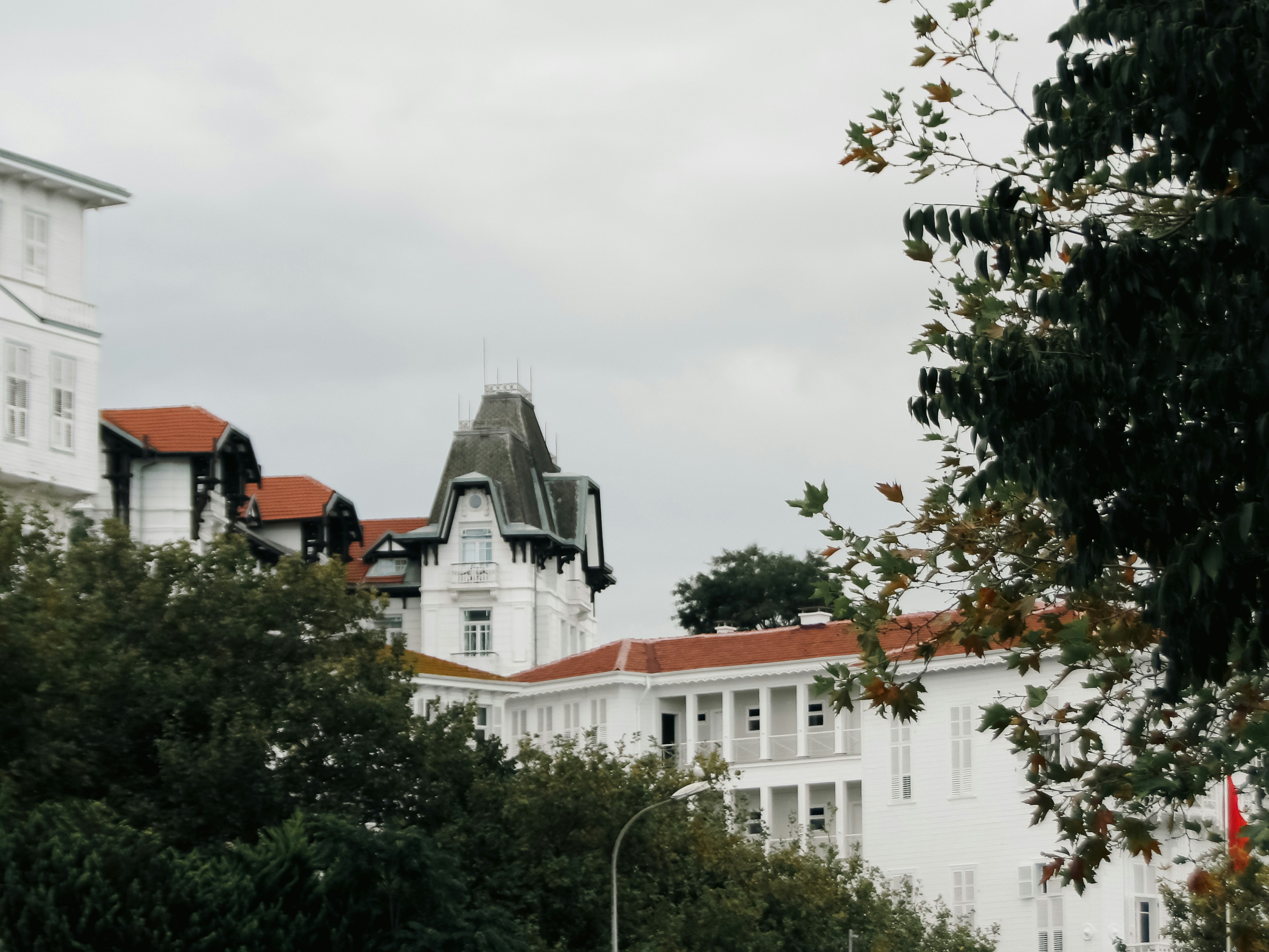 White institutional buildings with red-tiled roofs framed by trees under an overcast sky; a calm campus scene with classic architecture.