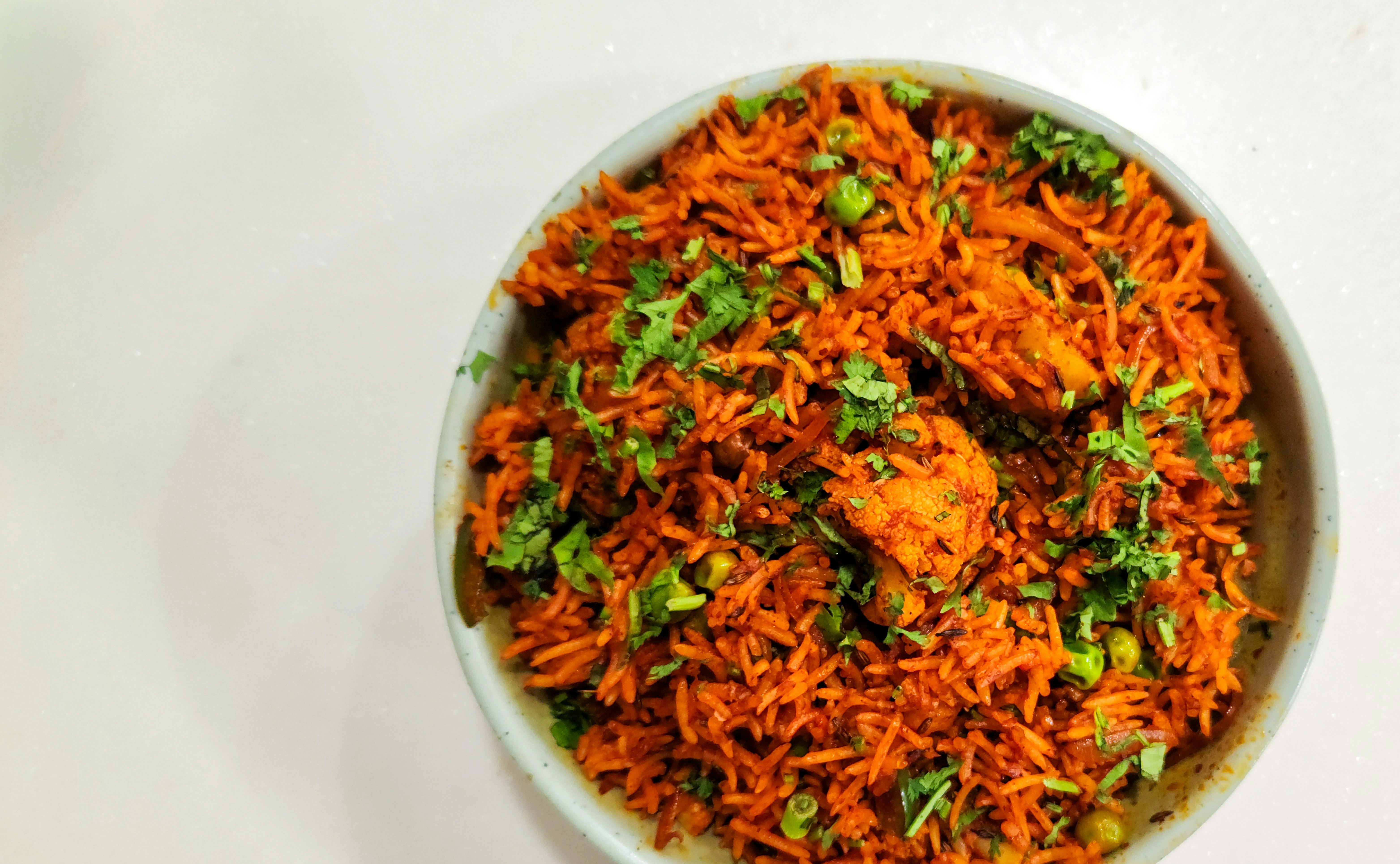 A plate of vibrant, wok-tossed Schezwan fried rice, glistening with aromatic oils and signature spicy red seasonings. As a popular staple of Indo-Chinese fusion cuisine, the dish combines cooked rice with finely chopped vegetables and pungent Schezwan sauce. Editorial publications, food blogs, recipe sites, and culinary features can use this image to illustrate popular fusion food trends, spicy street-style eating, or vibrant Asian-inspired home cooking.