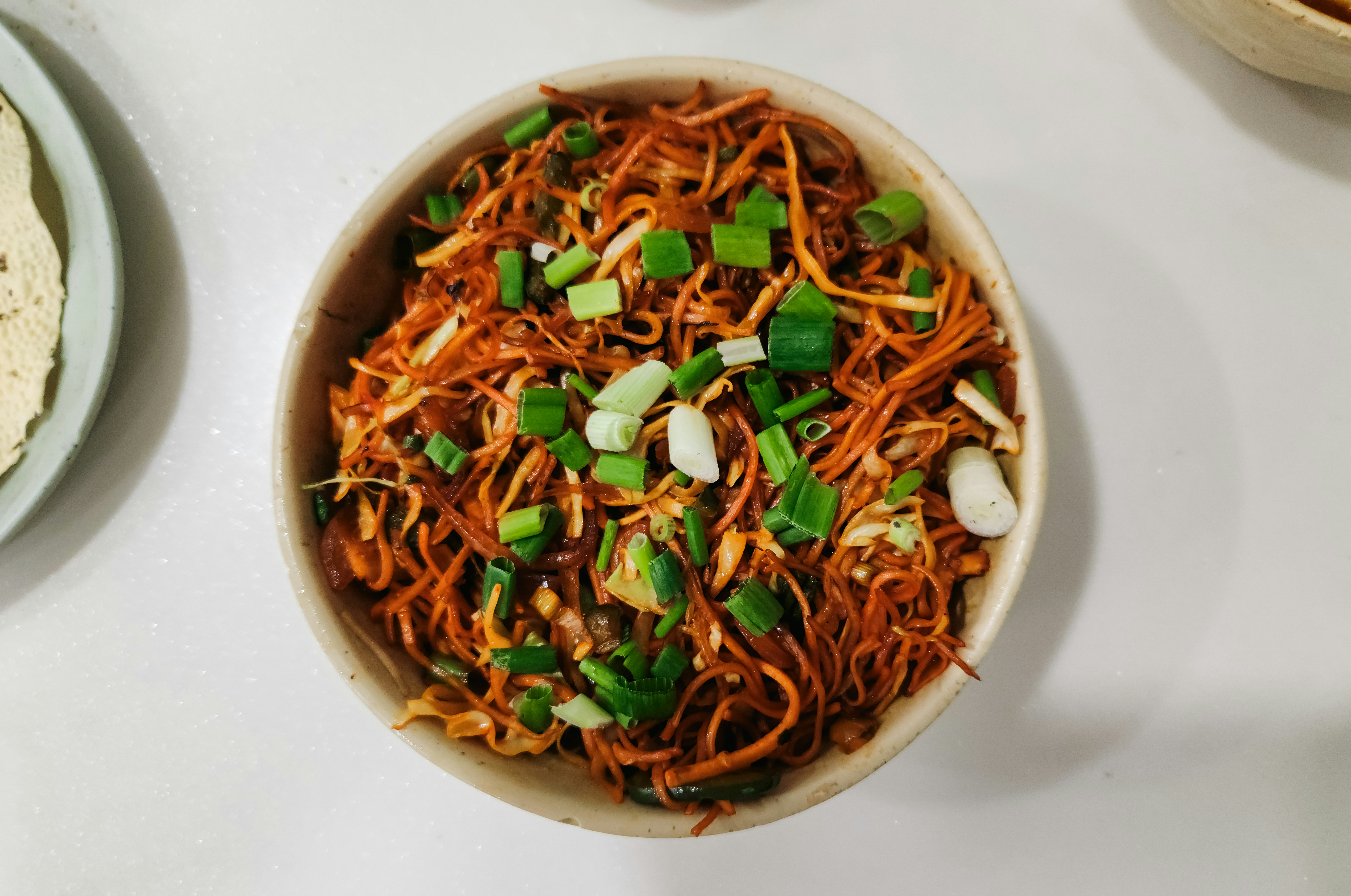 Wok-tossed Schezwan noodles coated in a vibrant, spicy red sauce and tossed with crisp mixed vegetables. As a favorite staple of Indo-Chinese fusion cuisine, the dish combines bold chili flavors with aromatic stir-frying techniques. Editorial publications, food blogs, recipe sites, and culinary features can use this image to illustrate popular fusion food trends, spicy street-style eating, or vibrant Asian-inspired comfort meals.