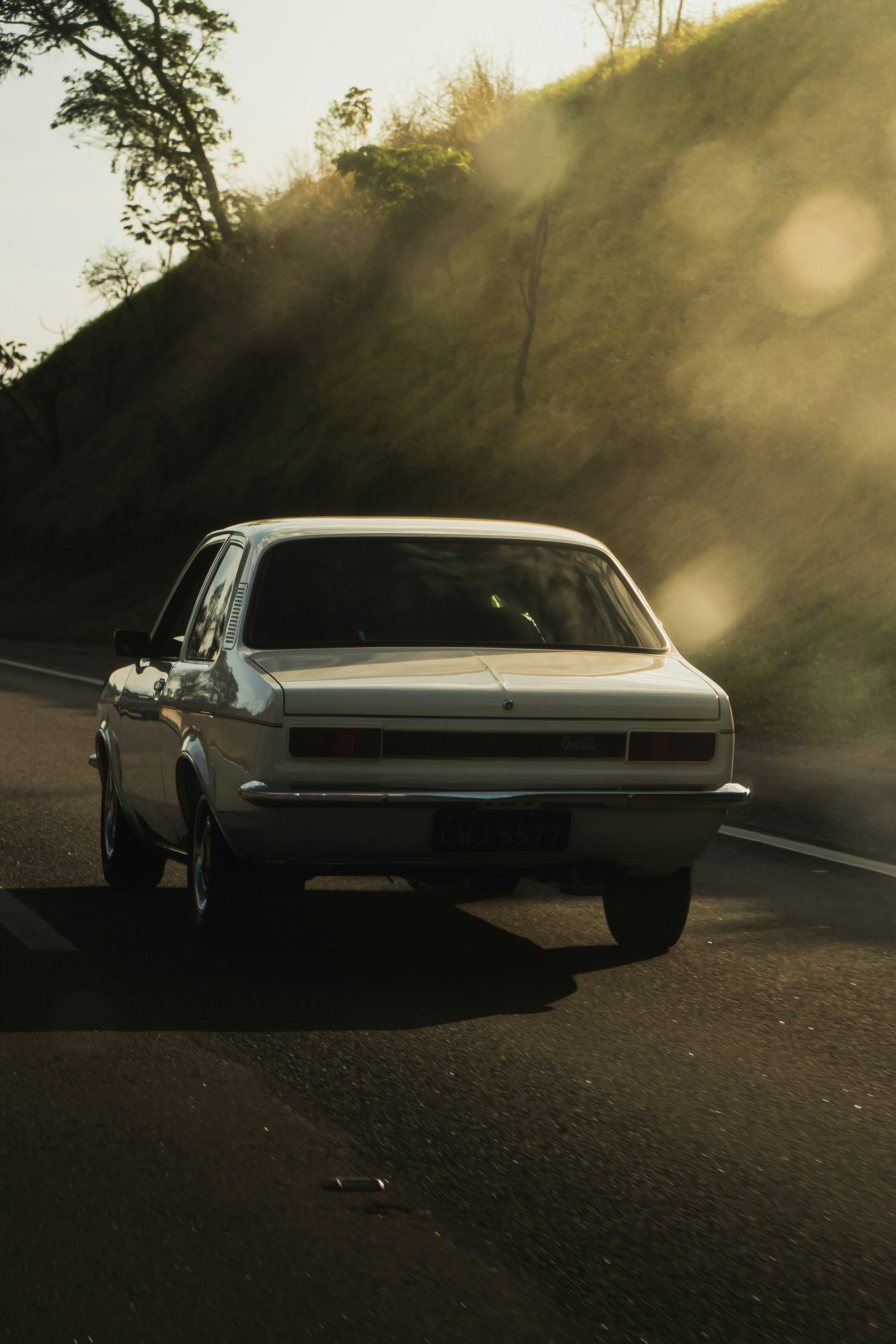 White vintage sedan on a sunlit hillside road