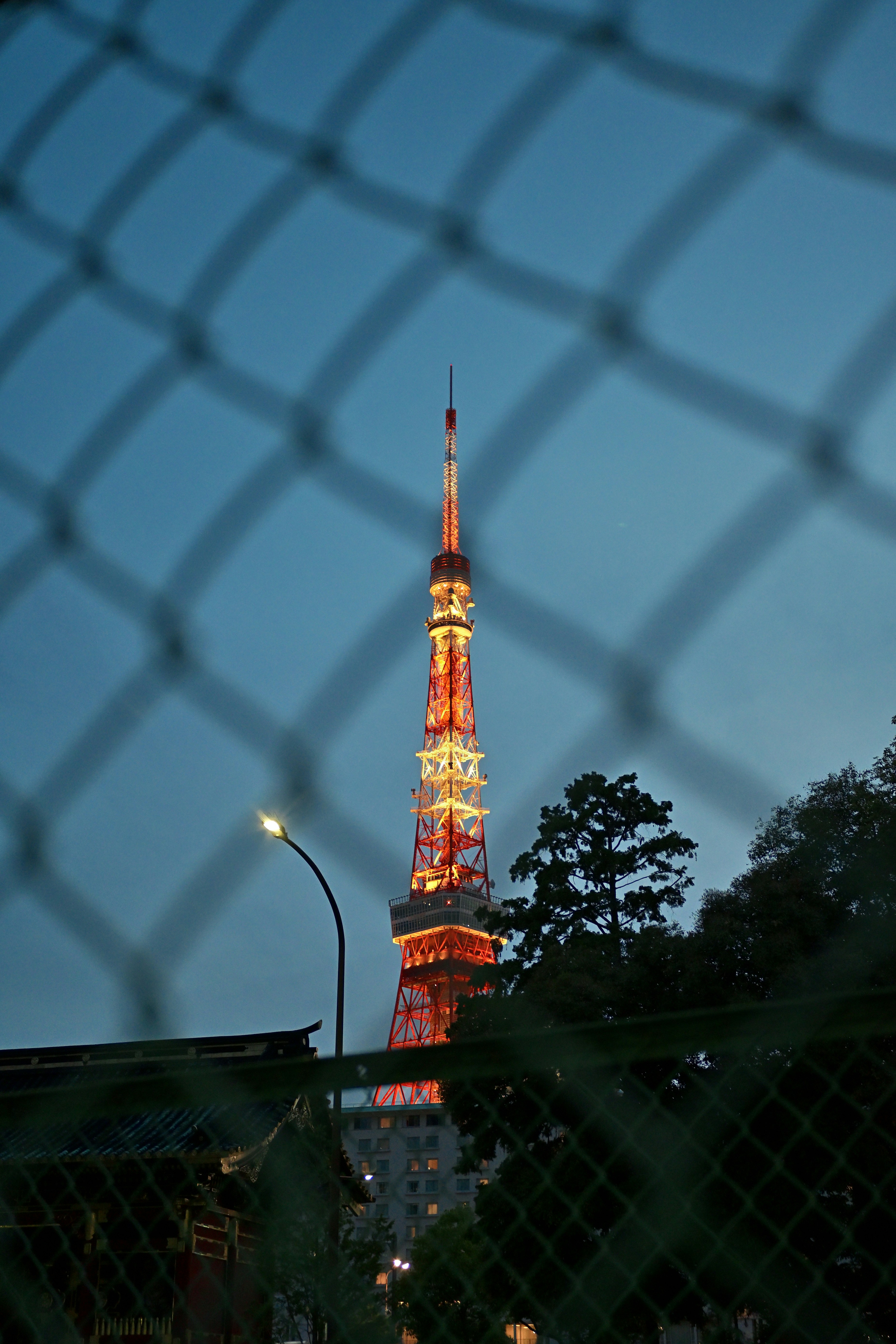 Red-and-White Tower Piercing the Evening Sky Beyond a Chain-Link Frame