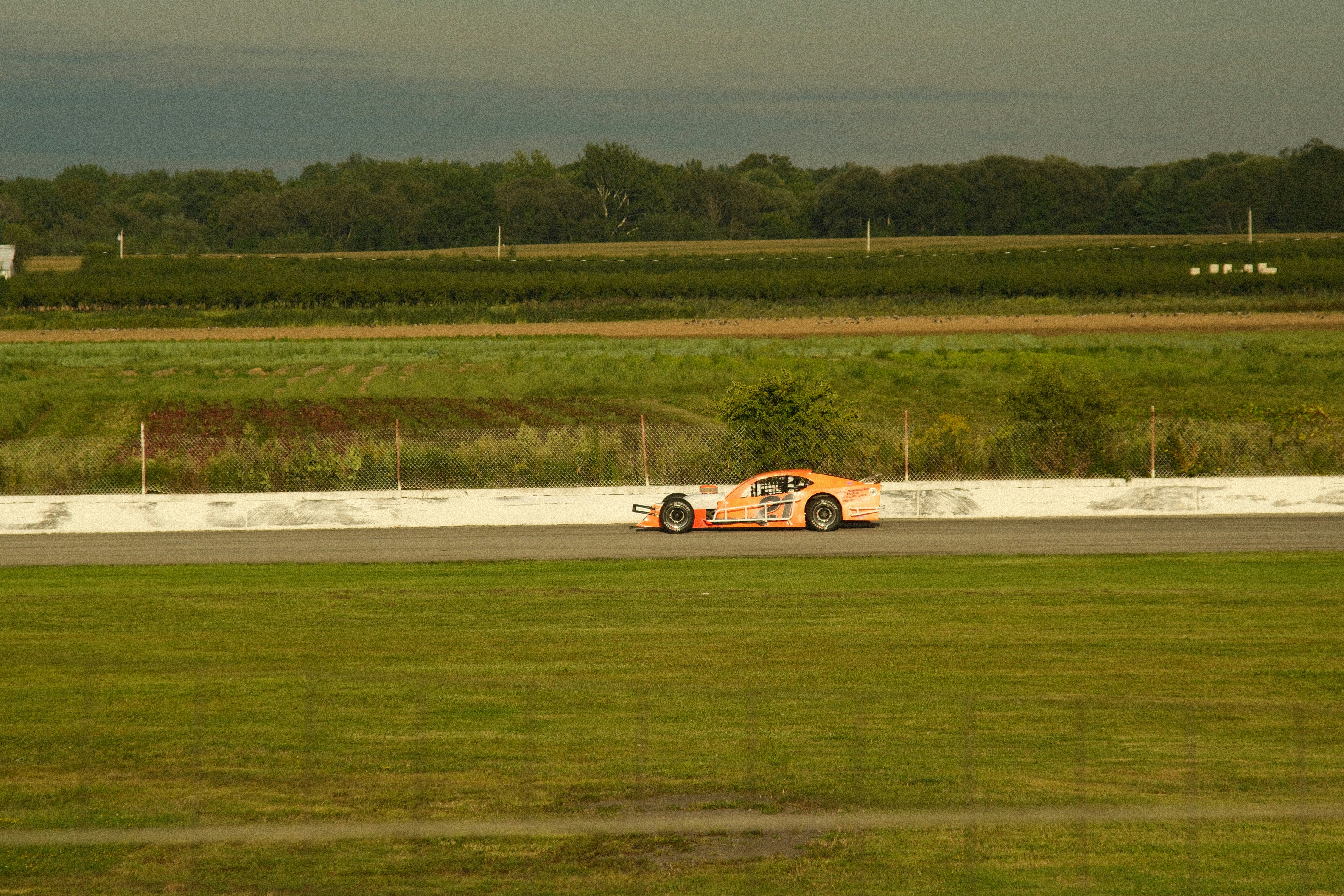 Orange race car blazing along a sunlit strip of track