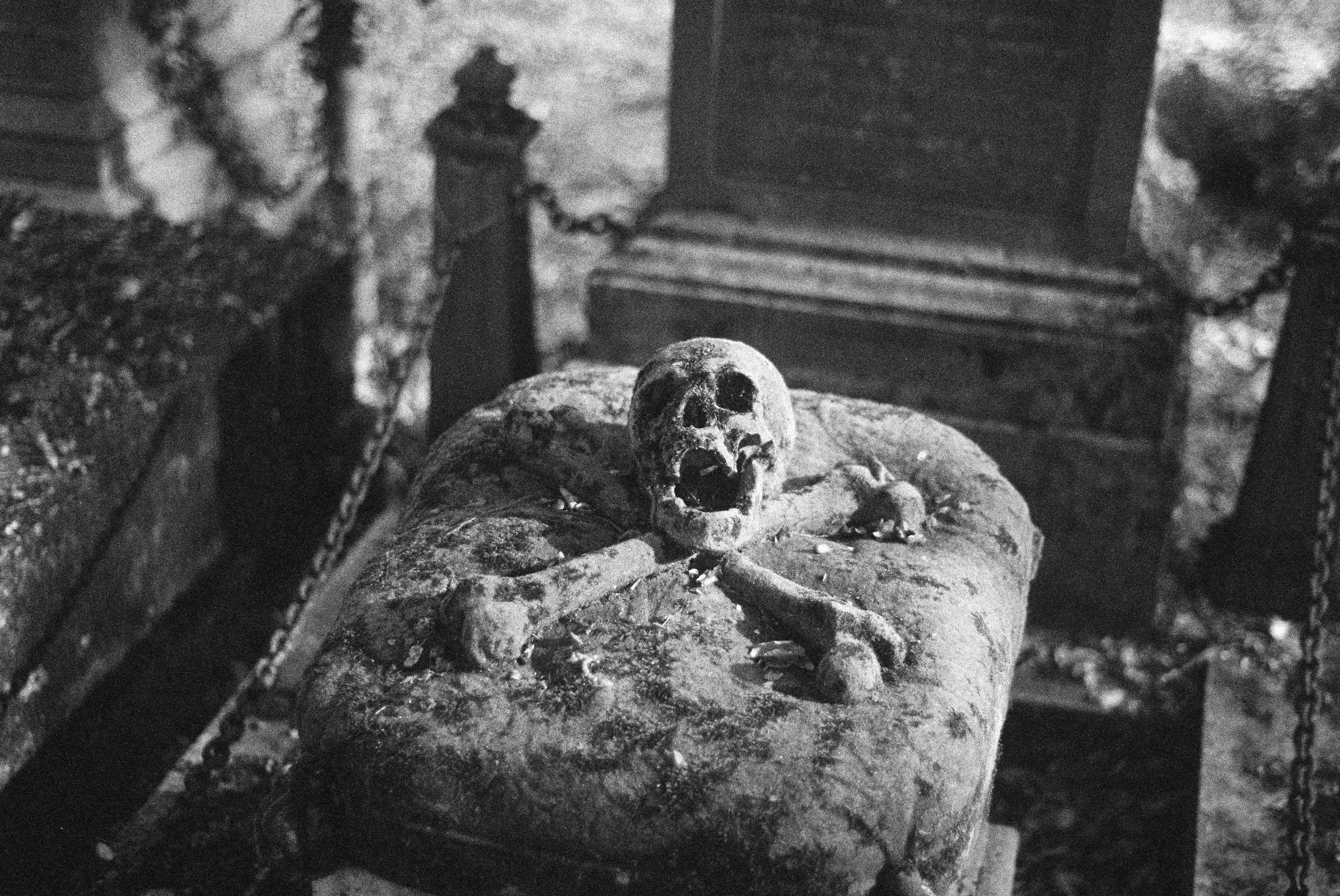 A weathered stone skull and crossbones carving on a grave marker in a cemetery