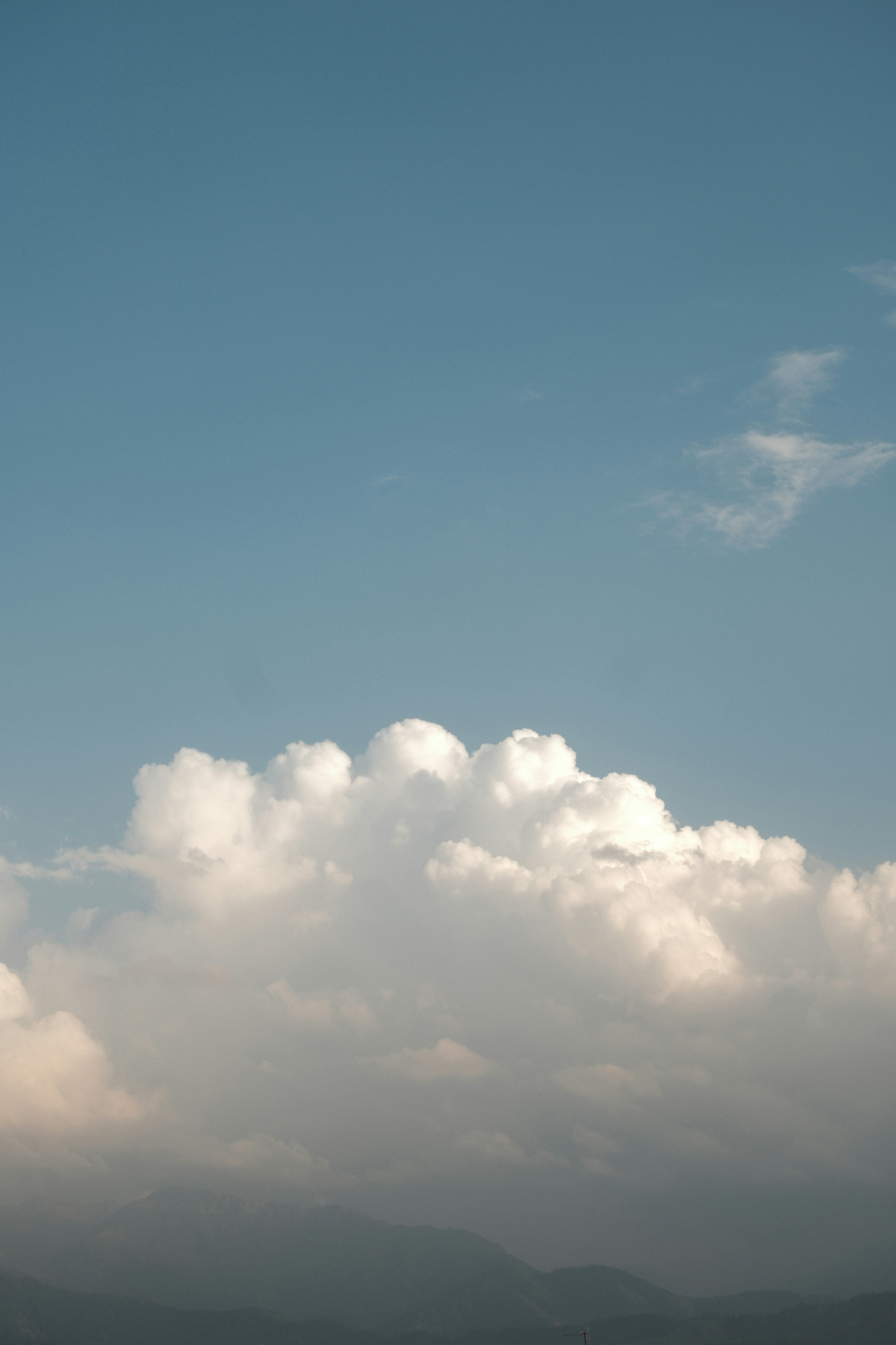 Soft, billowy clouds hover above a distant mountain range; the image emphasizes expansive sky and tranquil distance with a subtle horizon line.
