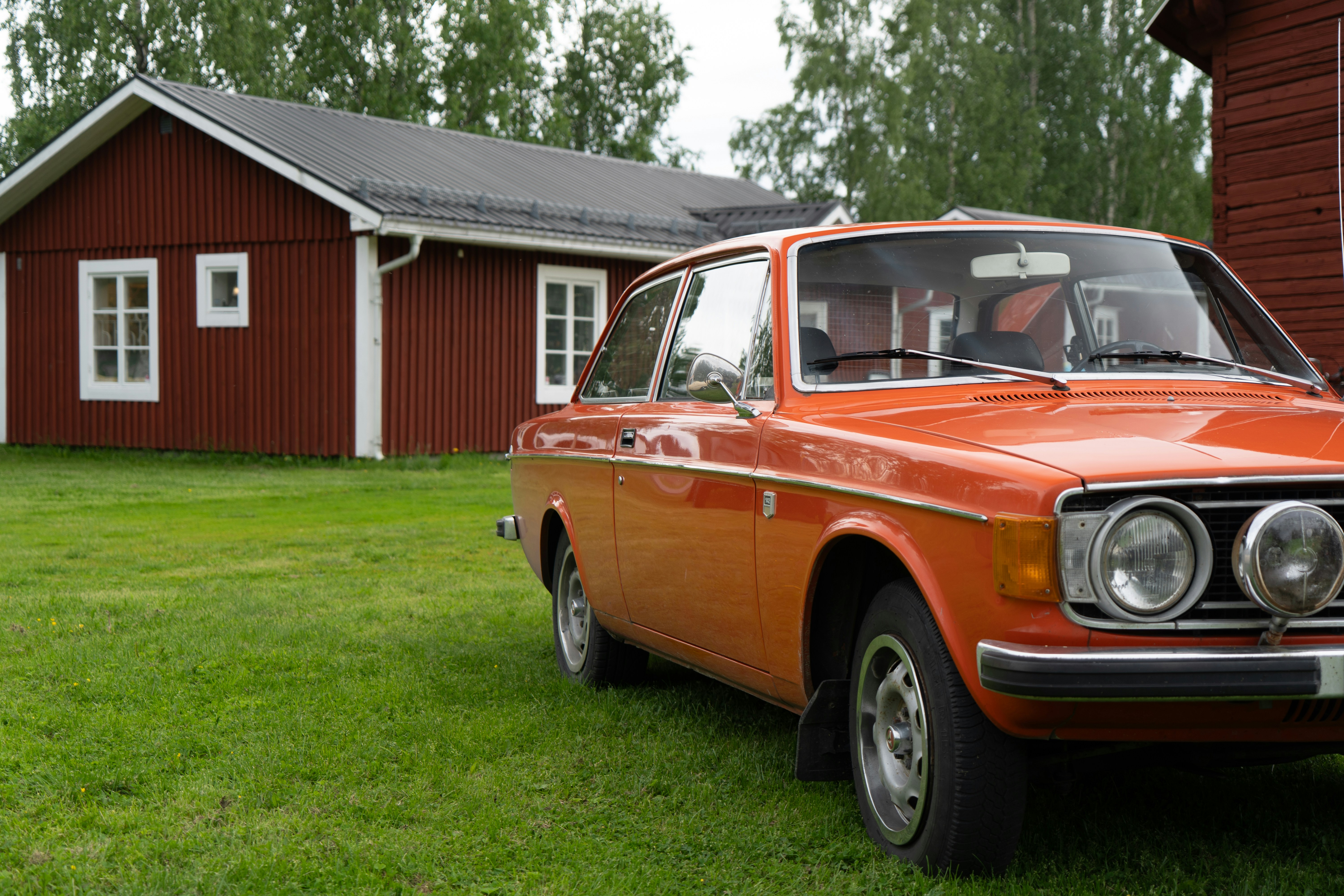 Orange Classic: A Retro Car Pauses Before a Red Barn