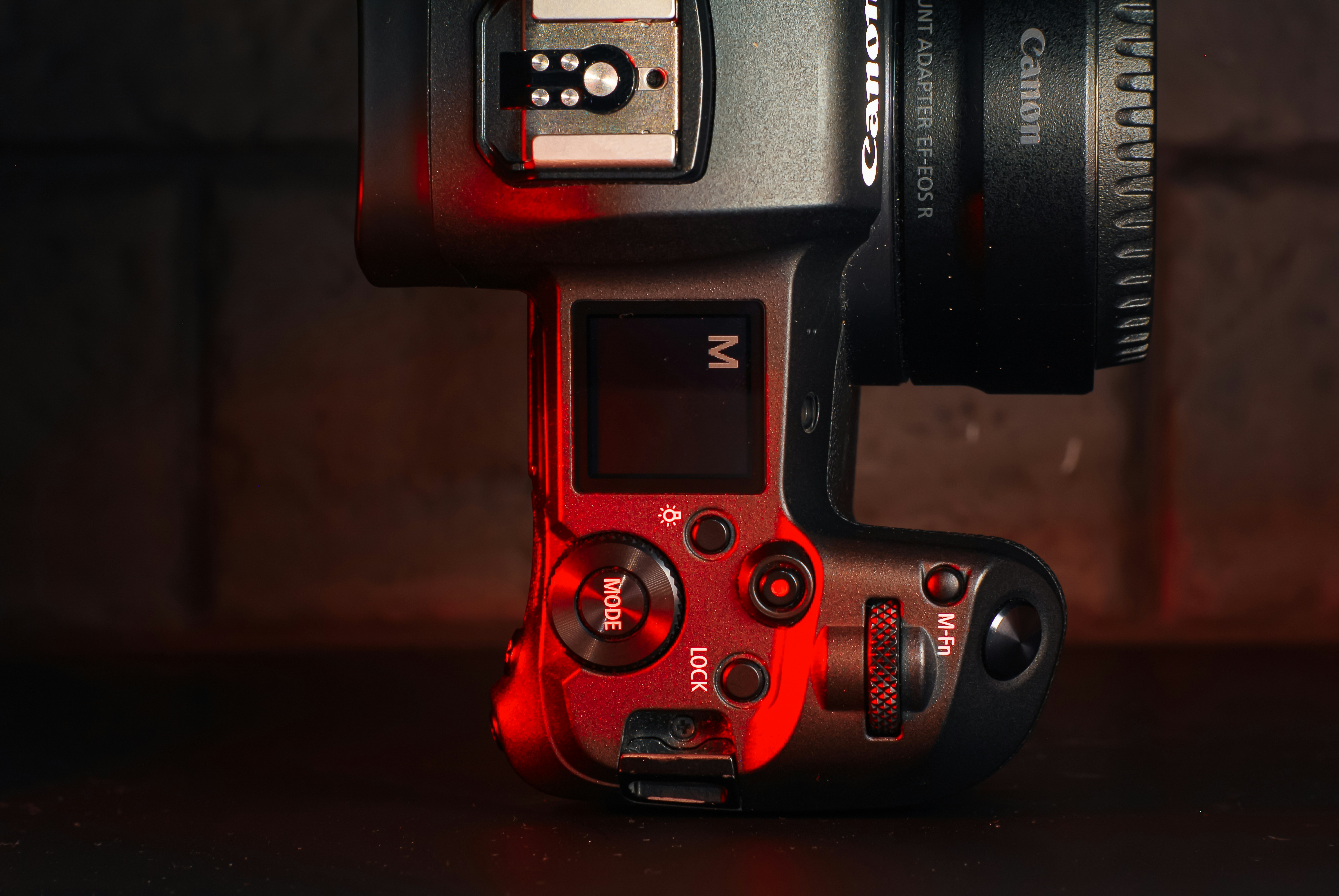 Close-up of a Canon camera body with red lighting highlighting the M-mode area, showcasing the grip and control dial against a dark background.