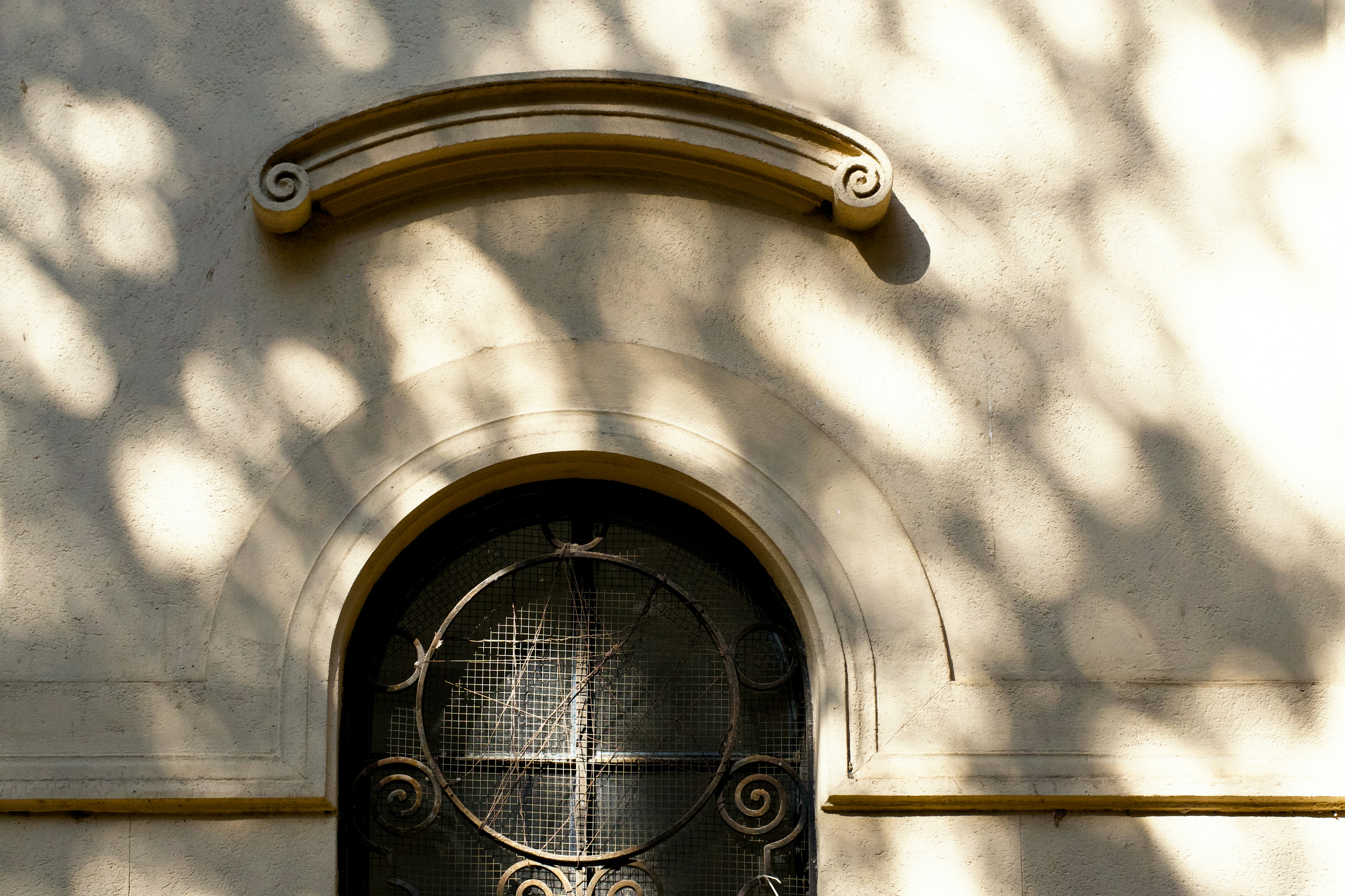 Arched Window Embellishment: Crescent Scrolls and Gridded Gate in Sunlit Facade