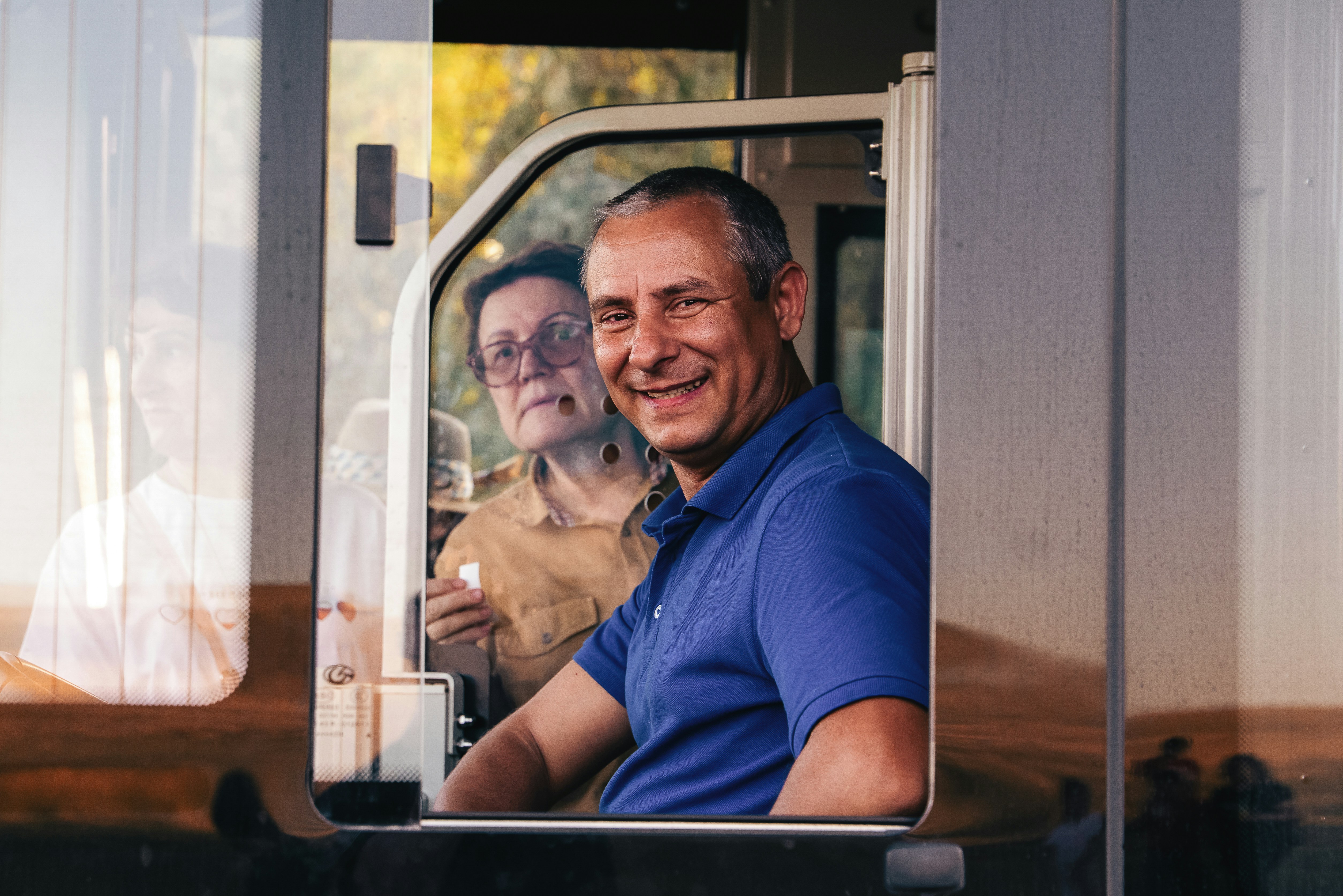 Smiling conductor with a passenger behind a bus window