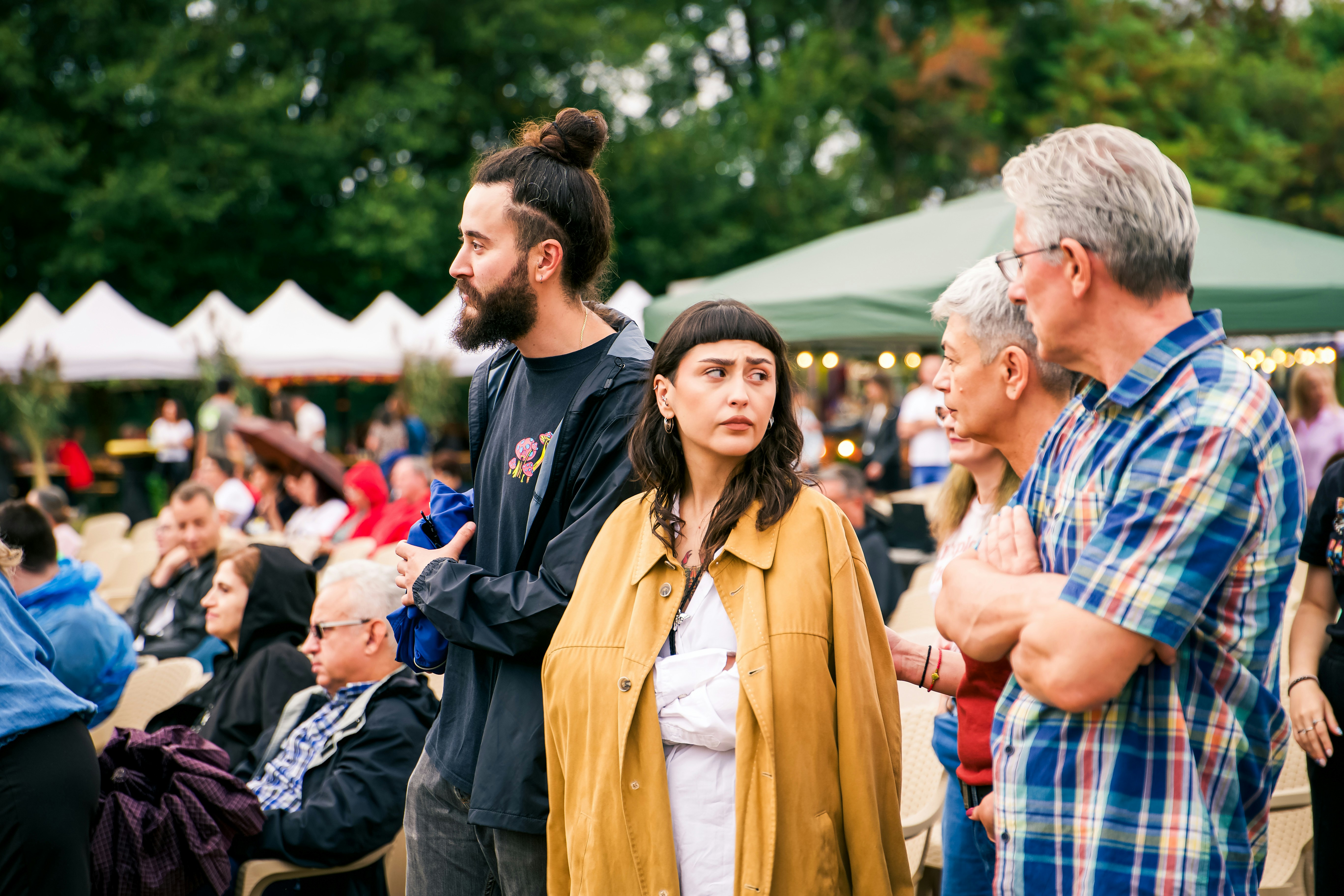 Center Stage at the Festival: A Woman in a Mustard Coat Among the Gathered Crowd